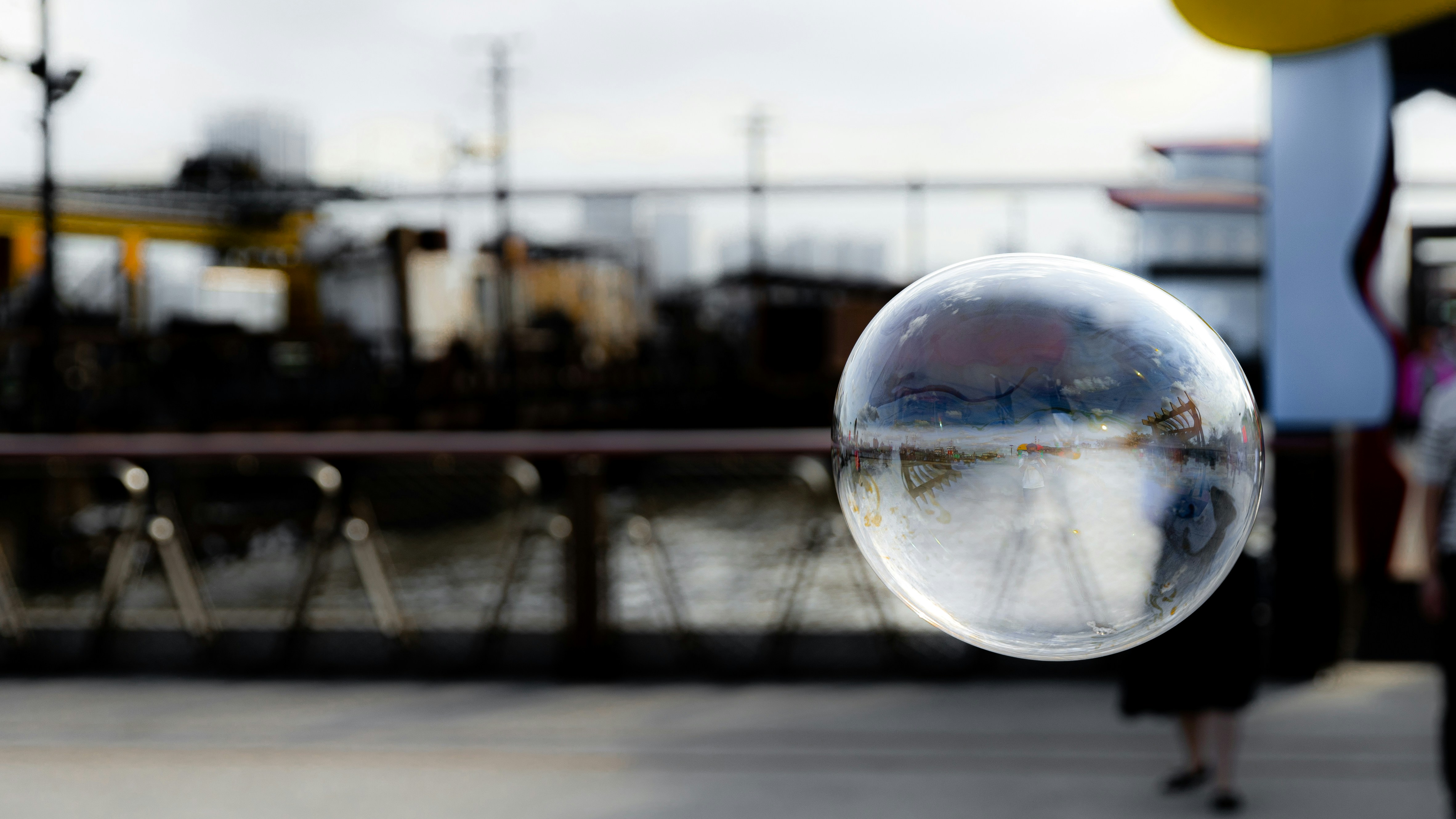 A large soap bubble suspended in mid-air, reflecting the surroundings with intricate details. The background features blurred urban elements, creating a whimsical contrast.
