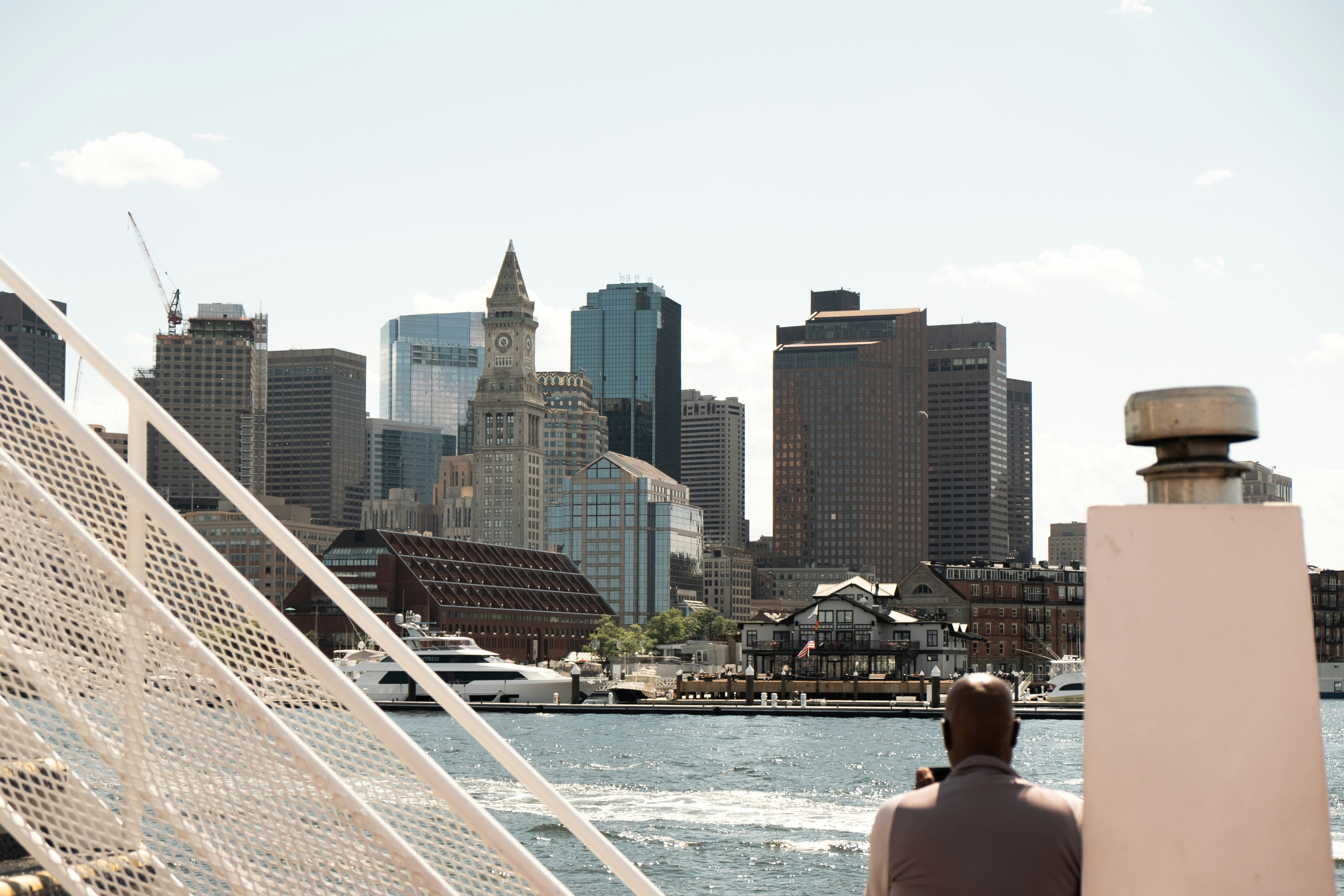 Man seated by the waterfront, gazing at the city skyline featuring modern and historic architecture. The scene captures the essence of urban life and leisure.