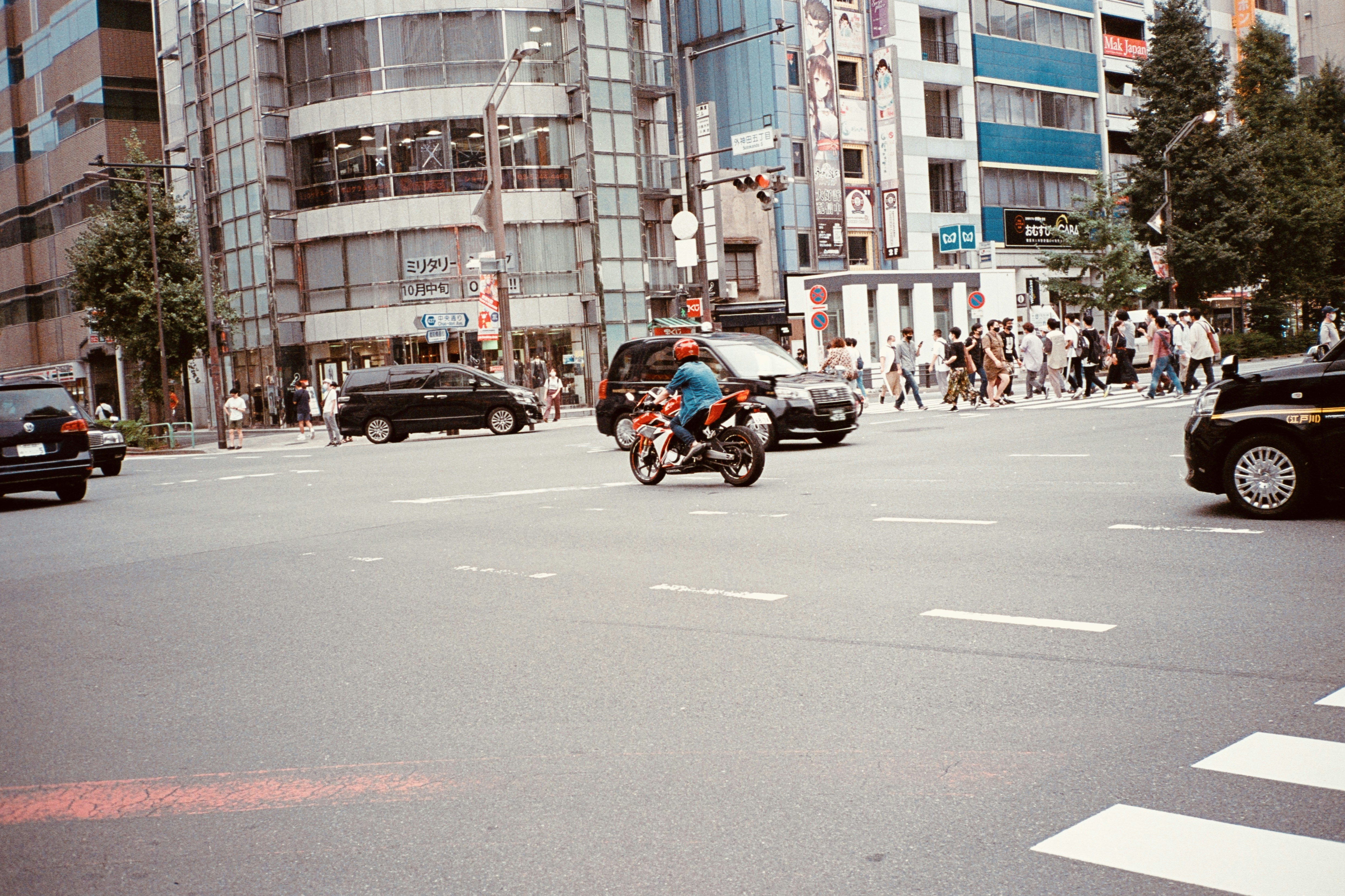 Motorcyclist navigating a busy intersection surrounded by cars and pedestrians in an urban setting.