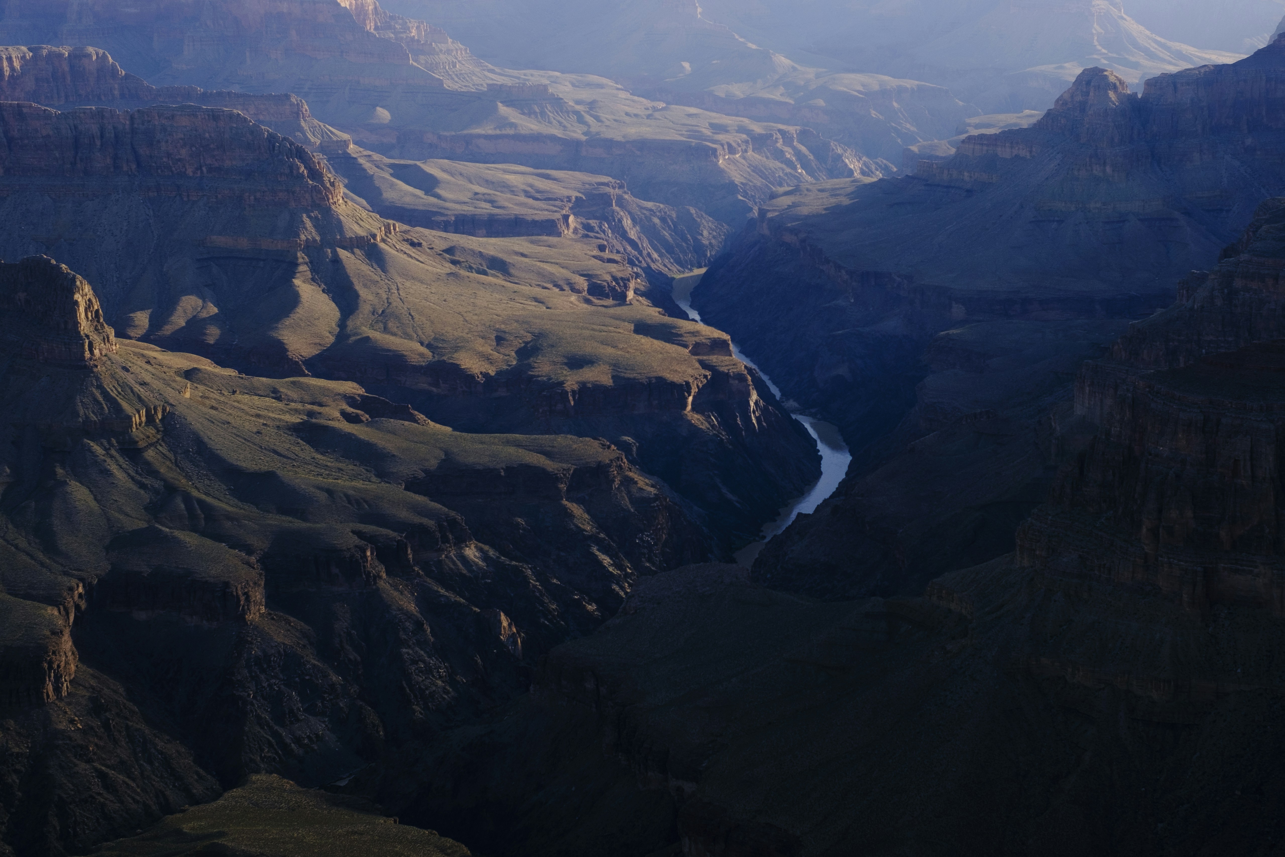 Aerial view of a winding river cutting through rugged canyon terrain, showcasing the interplay of light and shadow on the landscape.