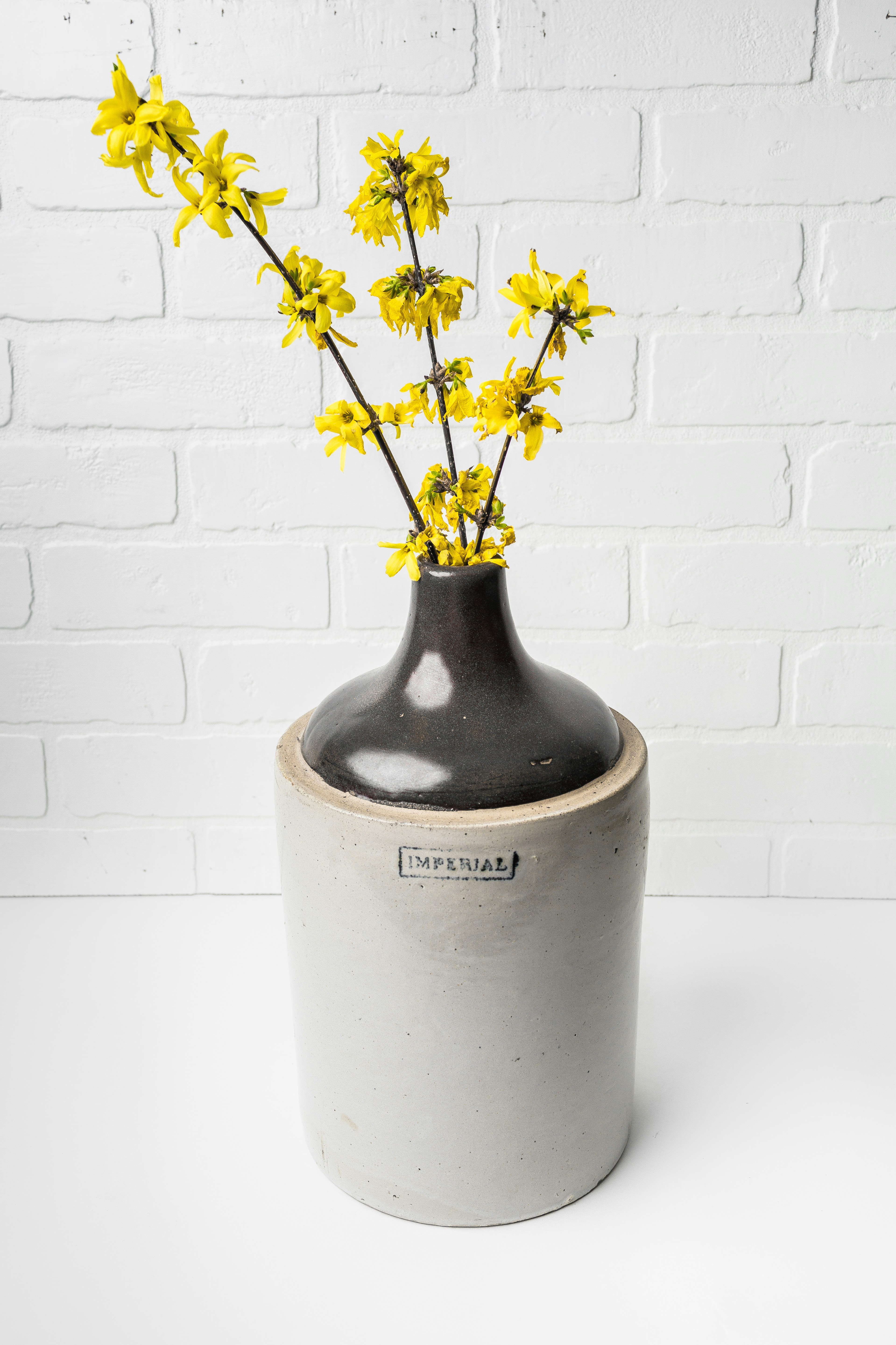 A sleek ceramic vase holds vibrant yellow flowers against a minimalist white brick background.
