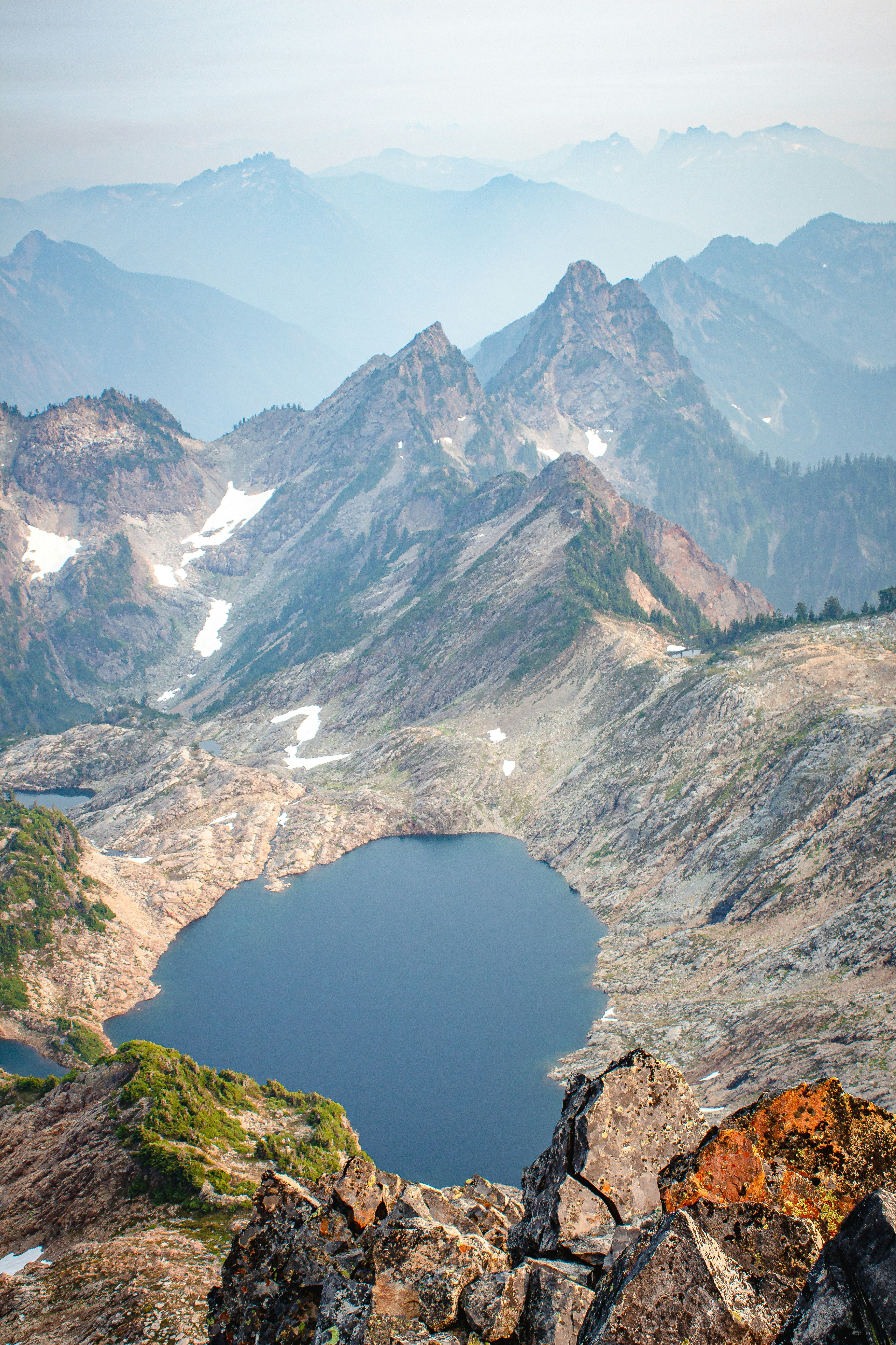 A tranquil mountain lake nestled between rugged peaks, surrounded by a tapestry of rocky terrain and verdant patches of forest.