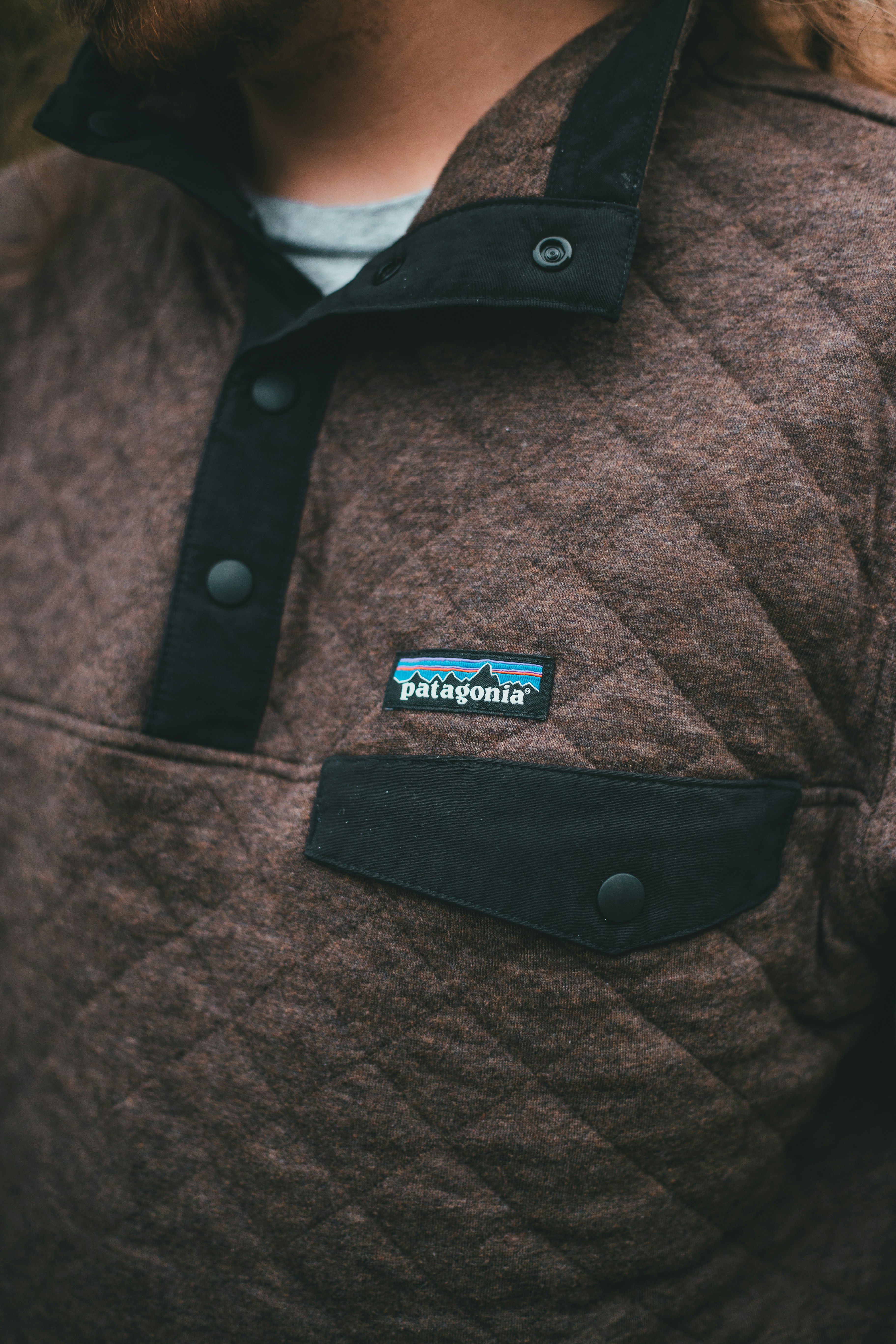 Close-up of a brown quilted Patagonia jacket featuring a chest patch and logo, emphasizing textured fabric.