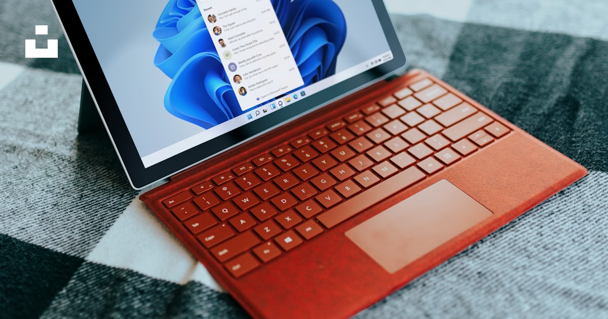 창가 체크 무늬 침대에 있는 빨간색 Surface 노트북 사진 Unsplash의 무료 마이크로 소프트 이미지