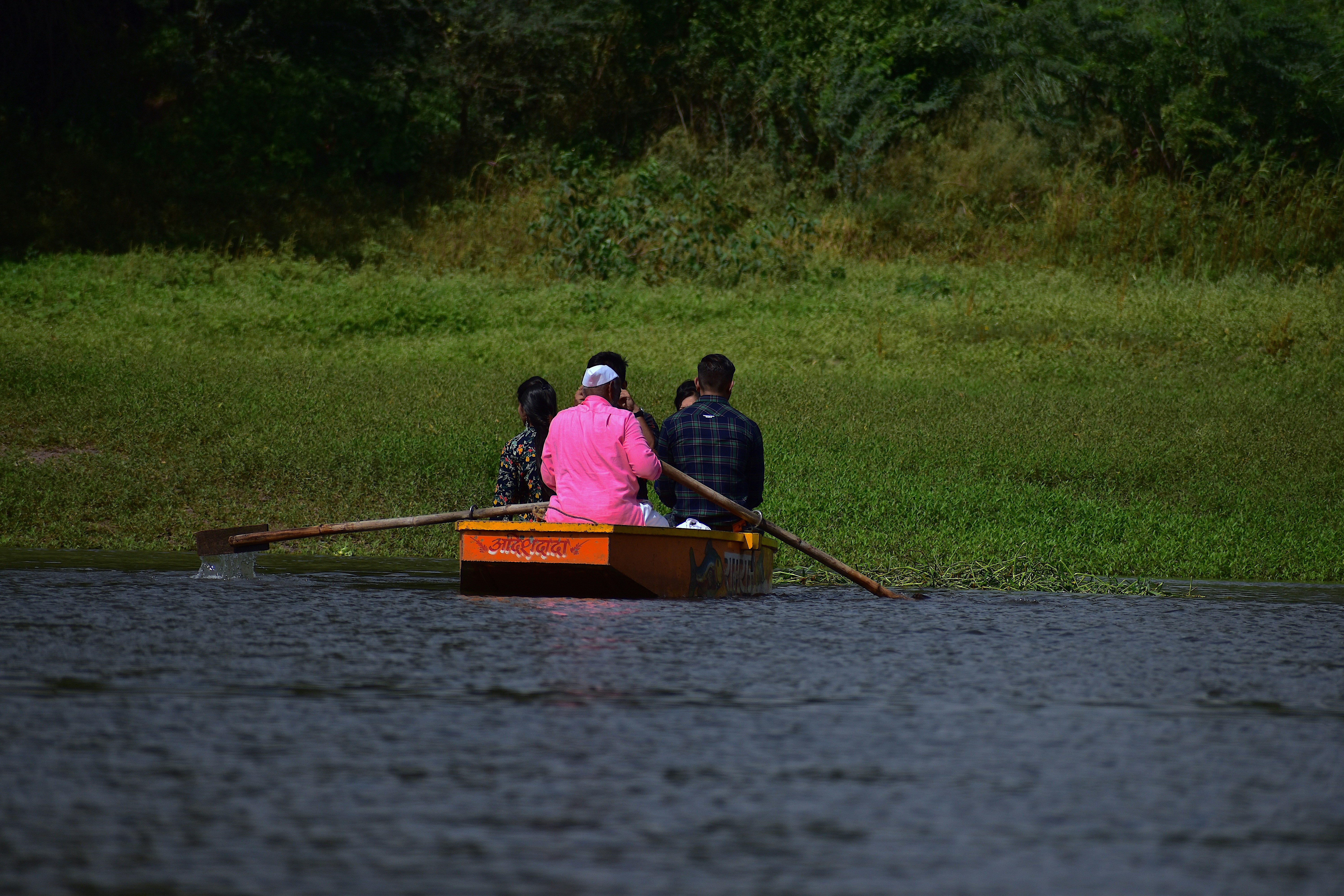Four individuals in a small boat navigate a tranquil lake, surrounded by lush greenery. The scene evokes a sense of calm and connection with nature.