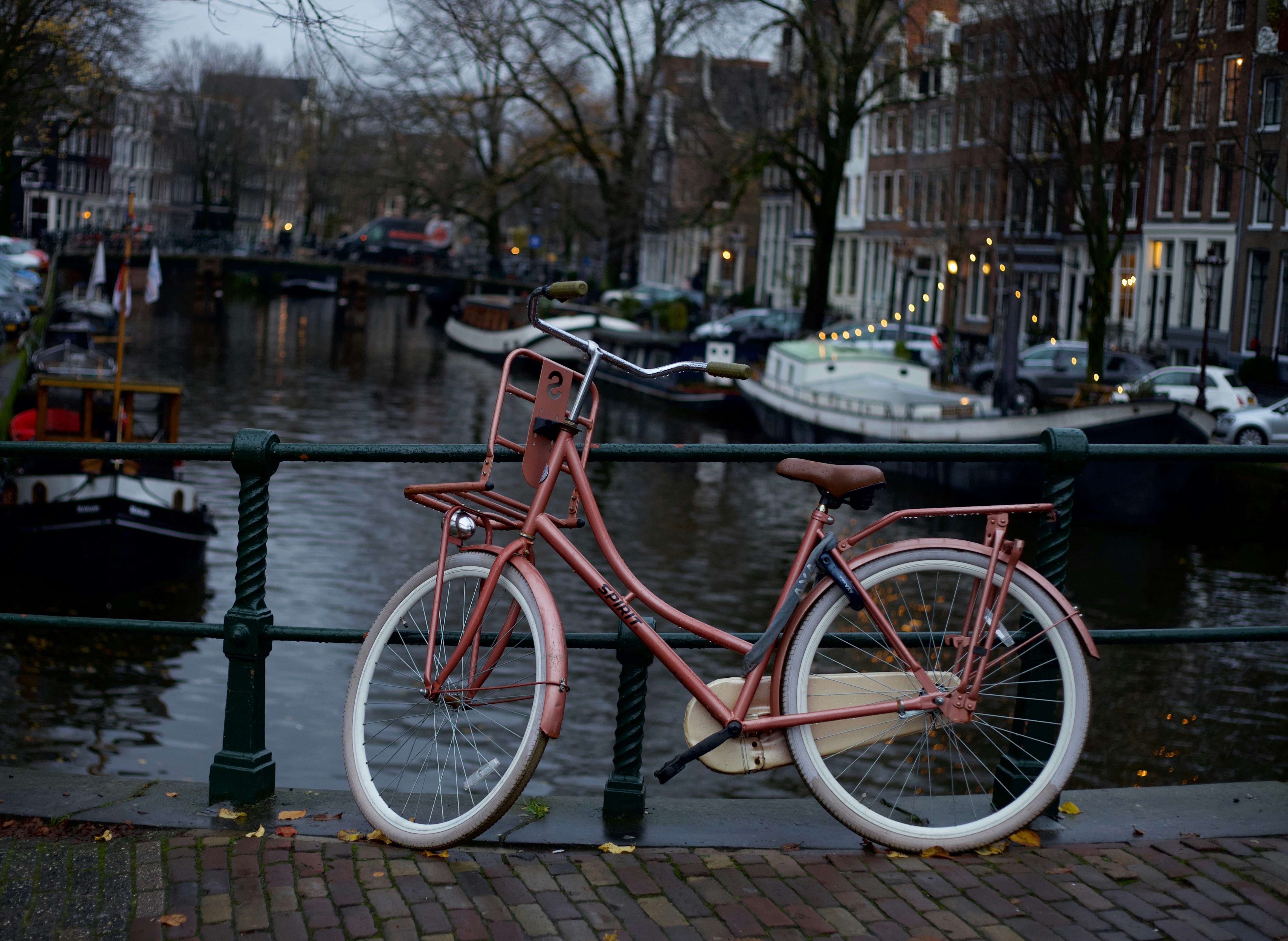 Vintage bicycle resting on a canal-side railing, surrounded by softly lit boats and trees in the background.