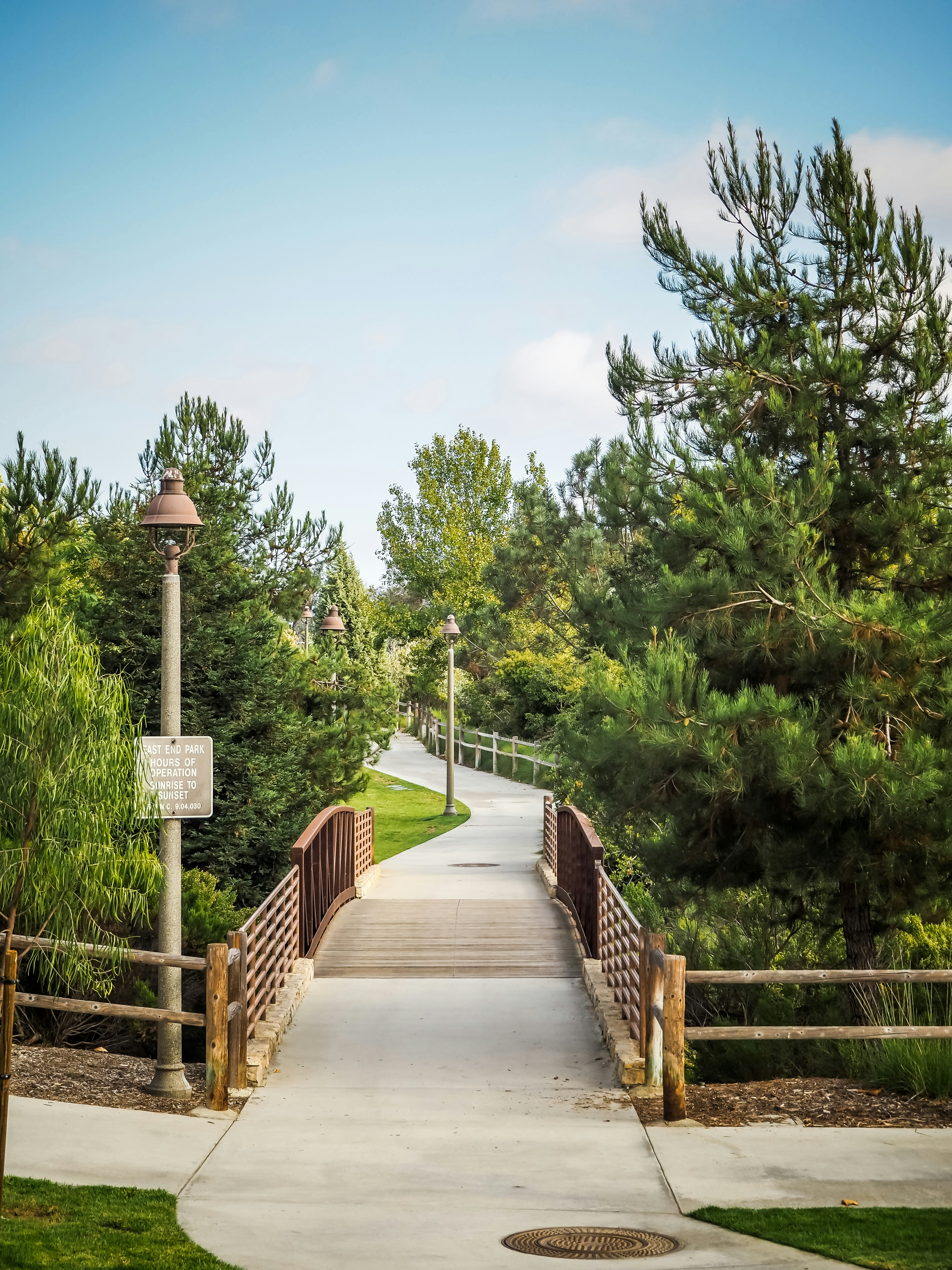 Winding pathway through a lush park, bordered by trees and decorative lamp posts, inviting visitors to explore the serene surroundings.