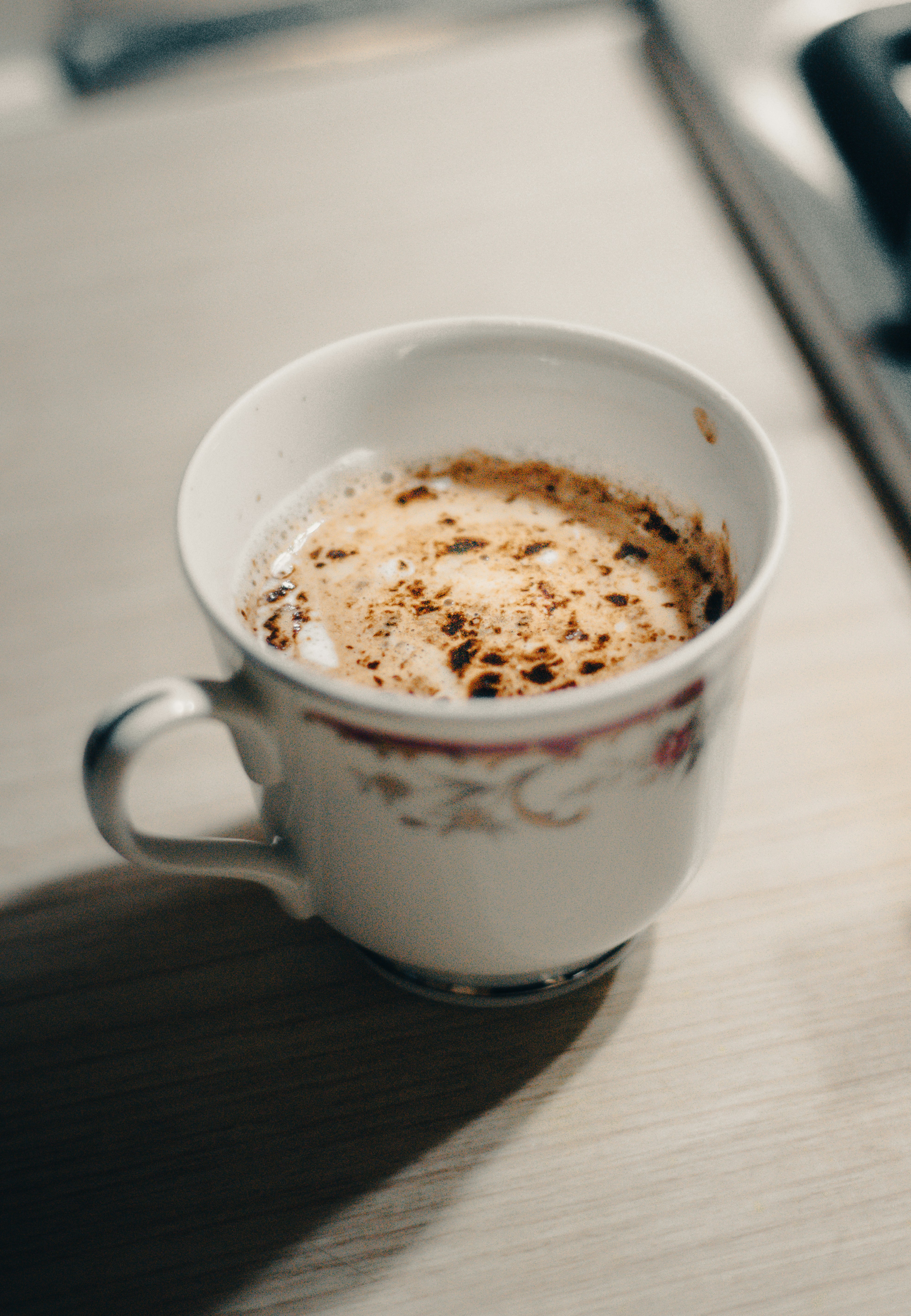A beautifully crafted cup of coffee sits on a wooden surface, showcasing a delicate floral design. The rich foam and sprinkled cocoa hint at a moment of indulgence.