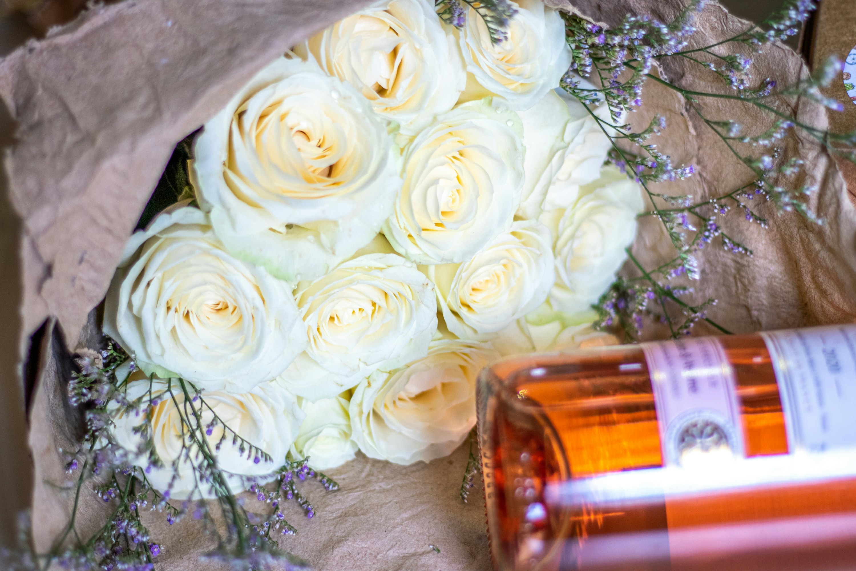 White roses wrapped in brown paper beside a bottle of rosé wine.