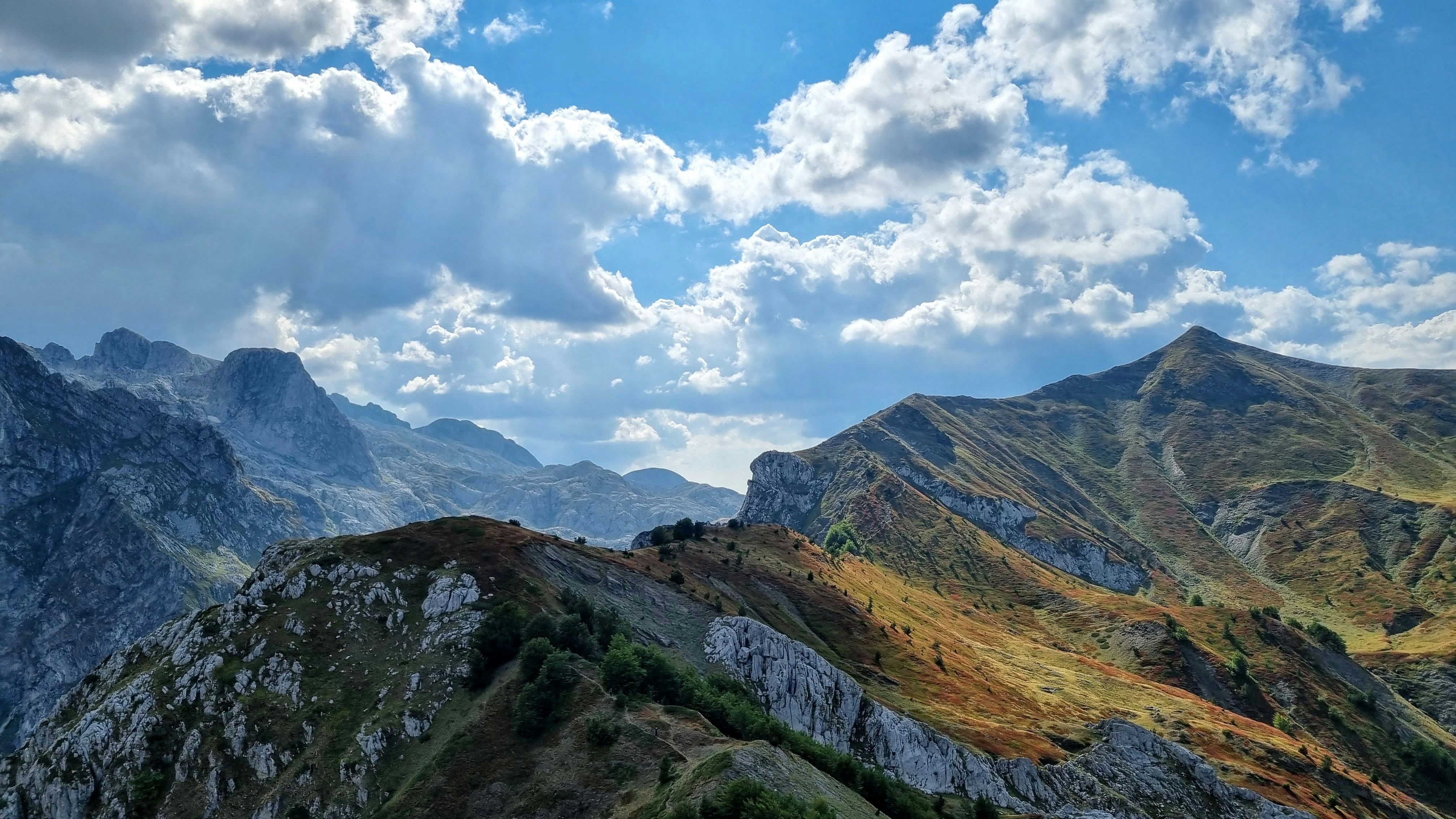 Mountain range with rugged peaks under a sky dotted with fluffy clouds.