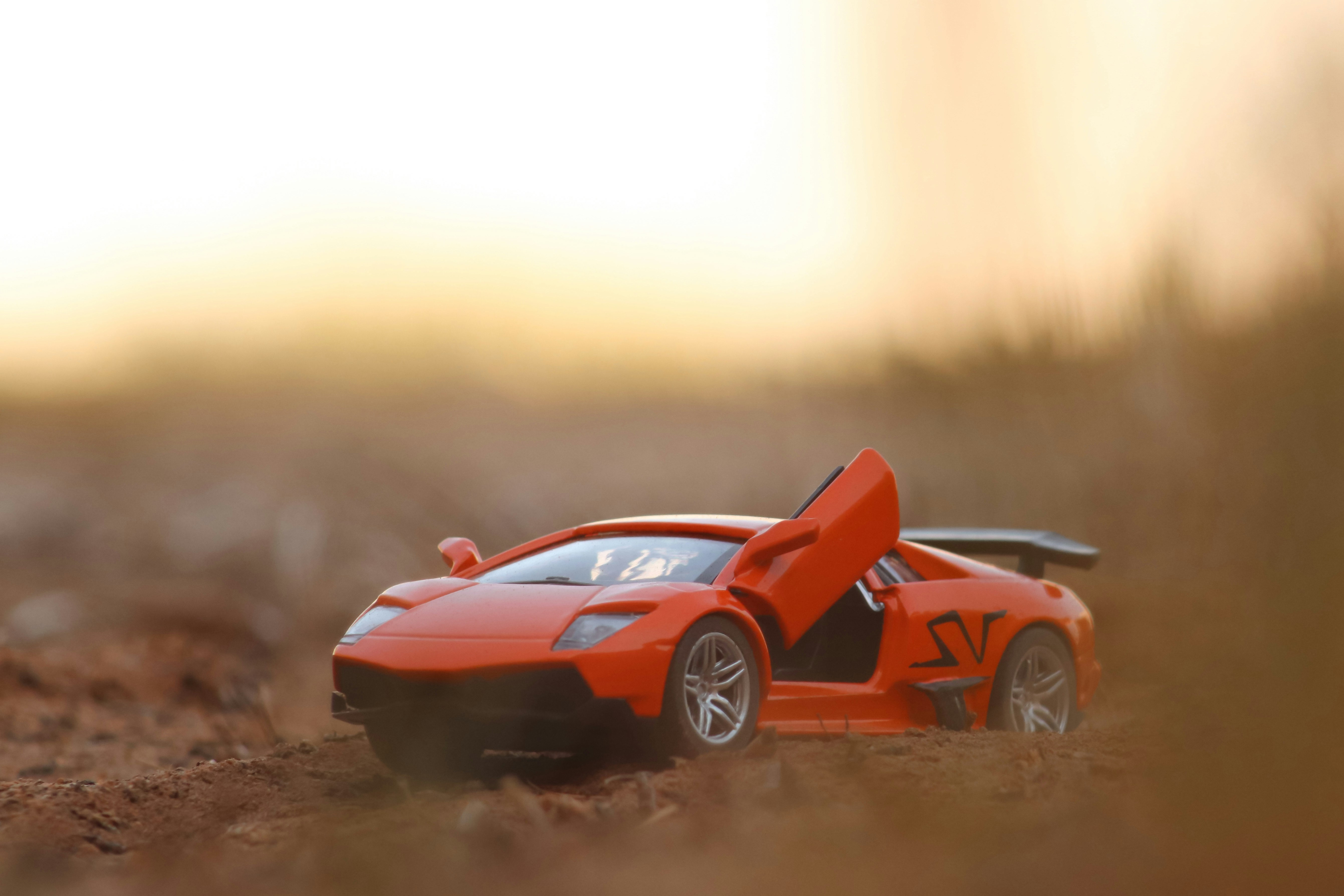 Orange toy supercar with scissor doors in a desert dusk