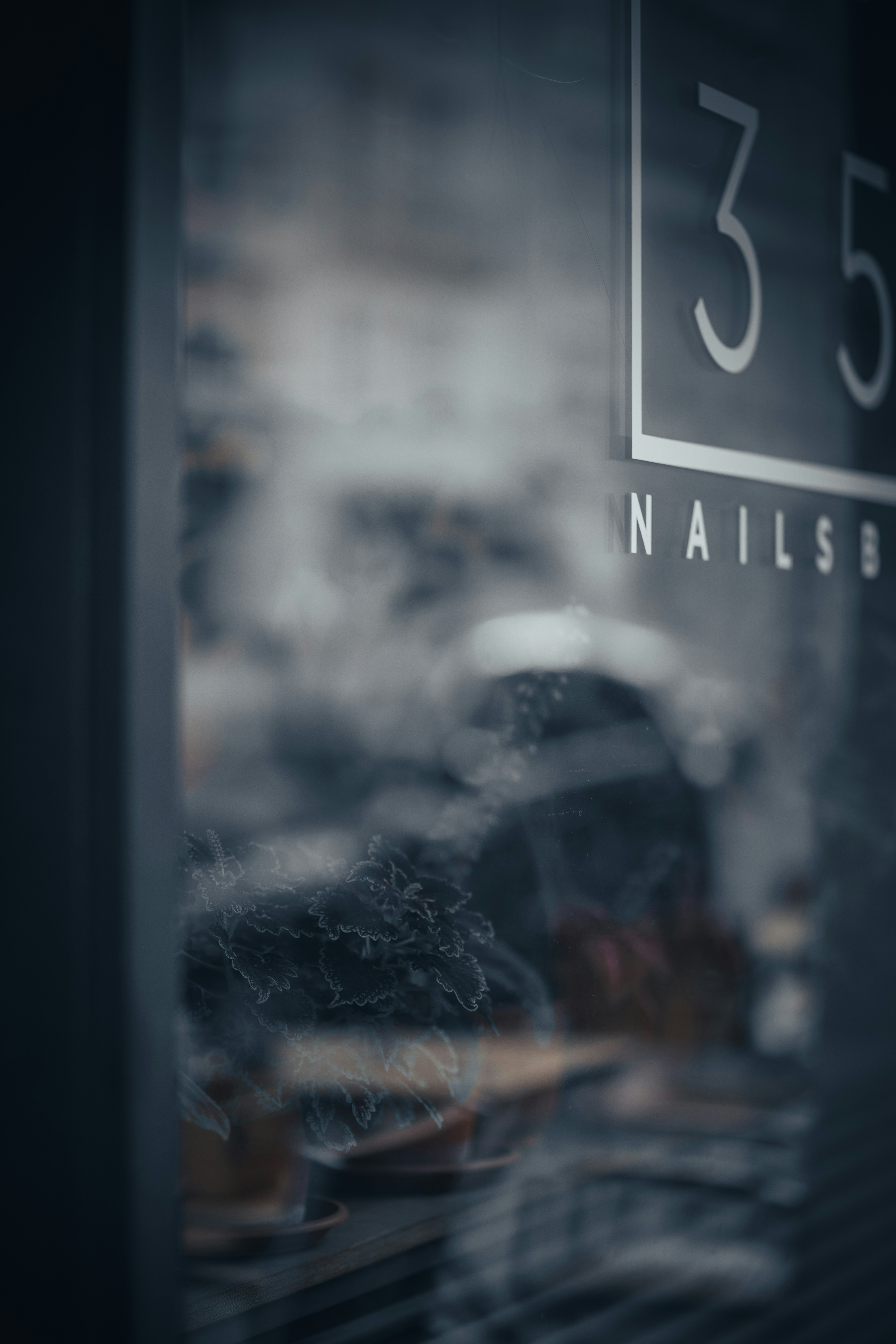 Moody storefront sign: 35 NAILS framed by blurred street reflections