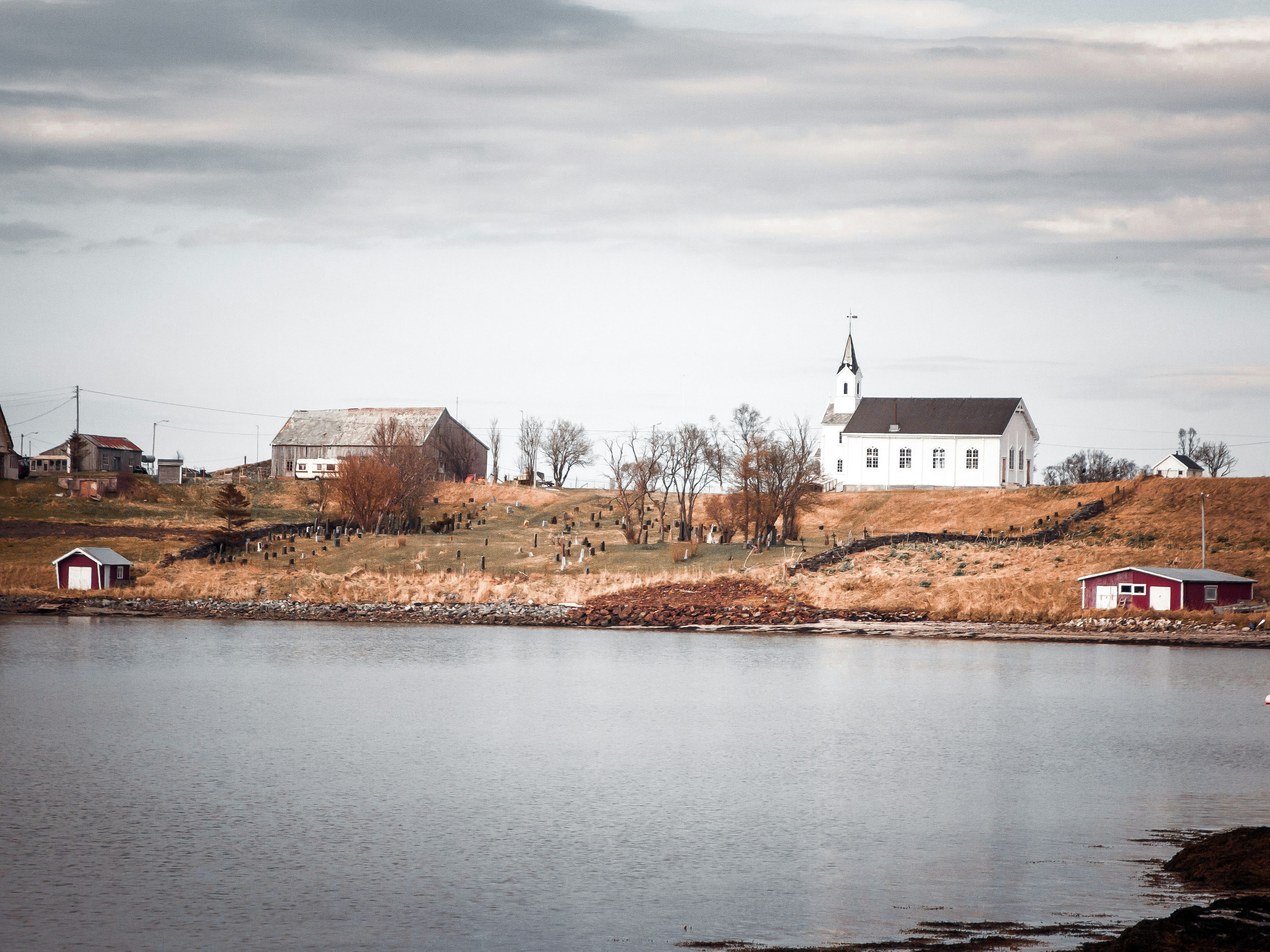 Quiet harbor village with white church and red boathouses across calm water