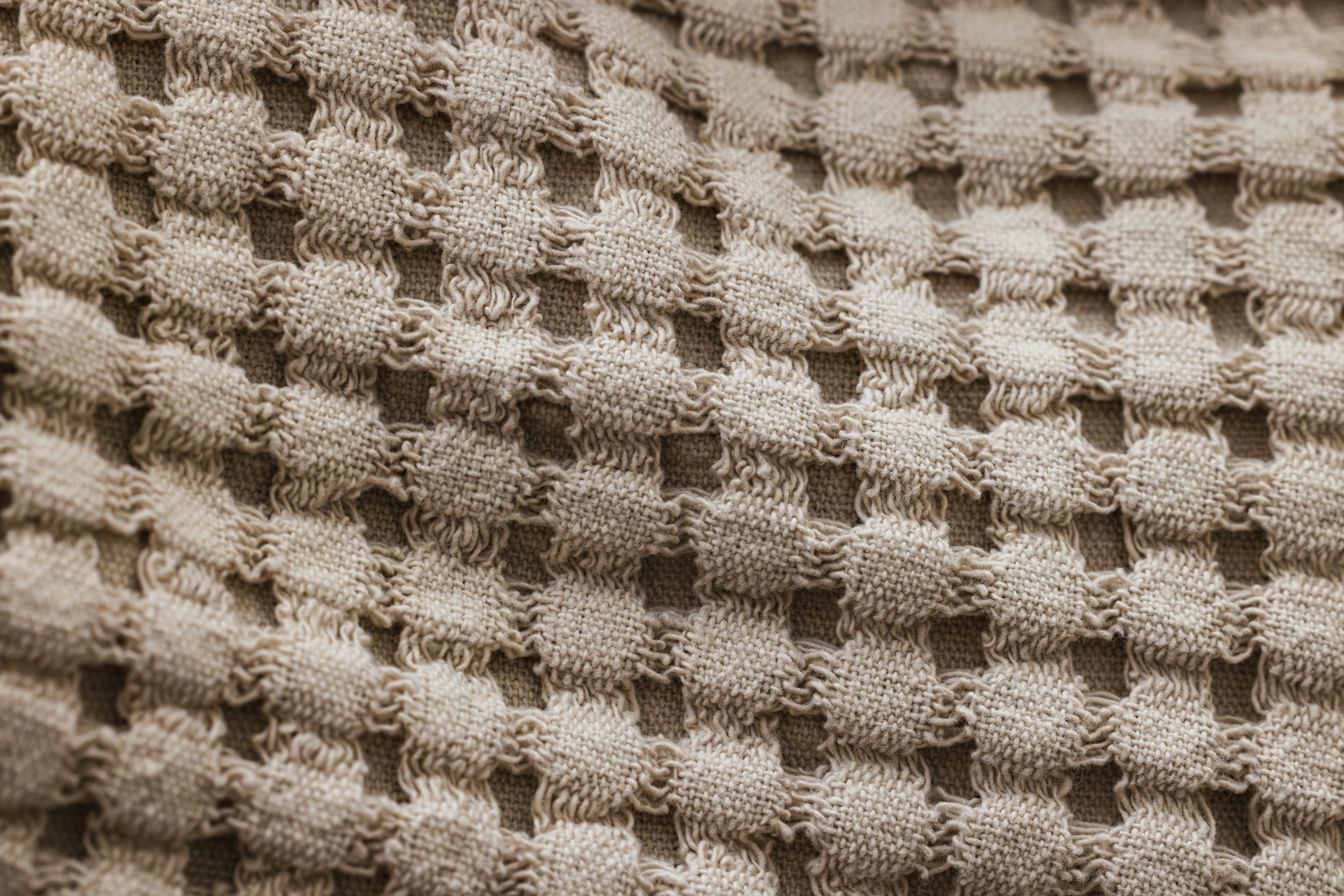 Close-up of a woven fabric showcasing intricate patterns and textures. The interplay of light and shadow enhances the tactile quality of the material.