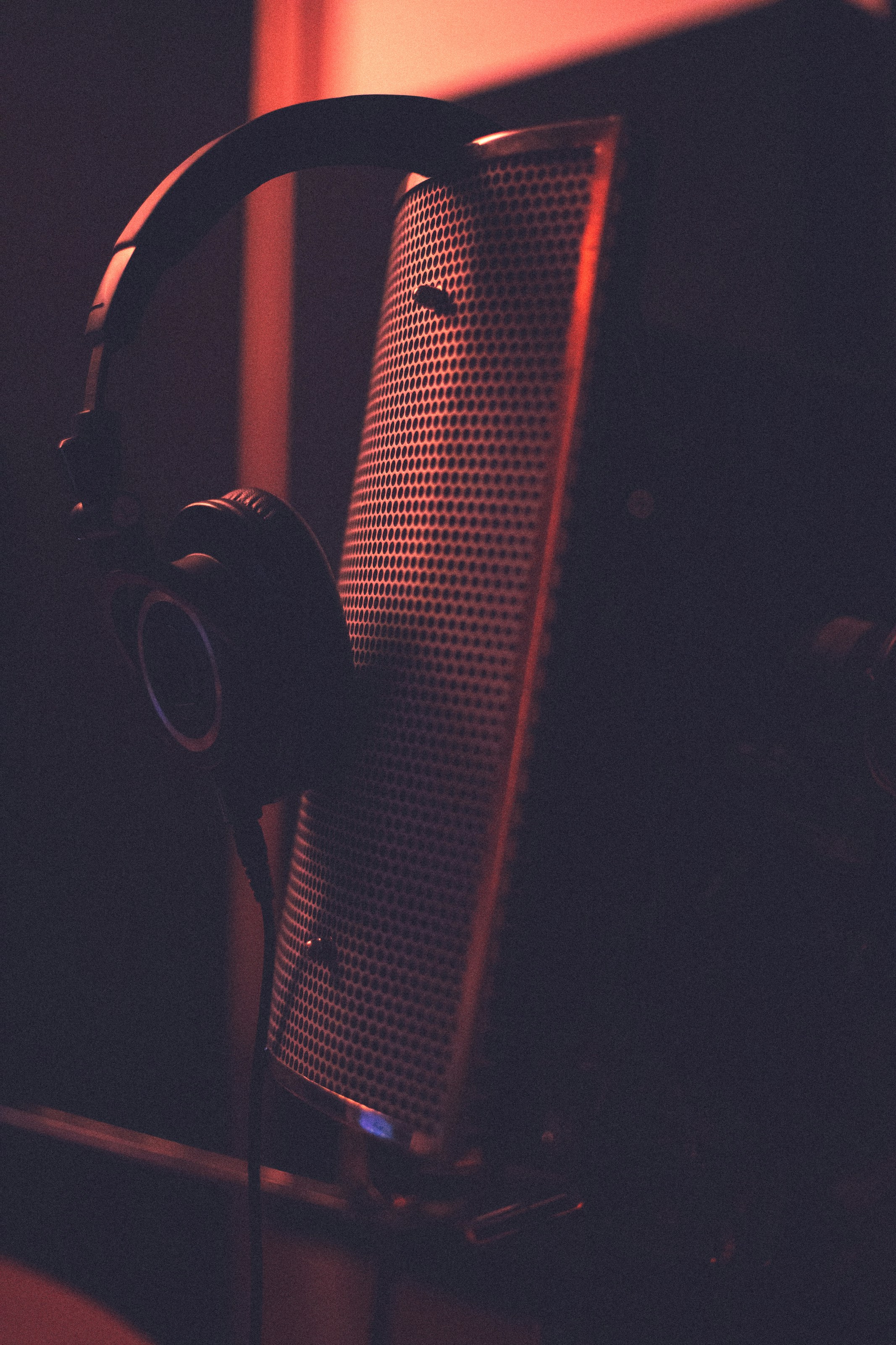 Microphone with headphones resting on it, illuminated by soft red lighting in a recording studio setting.