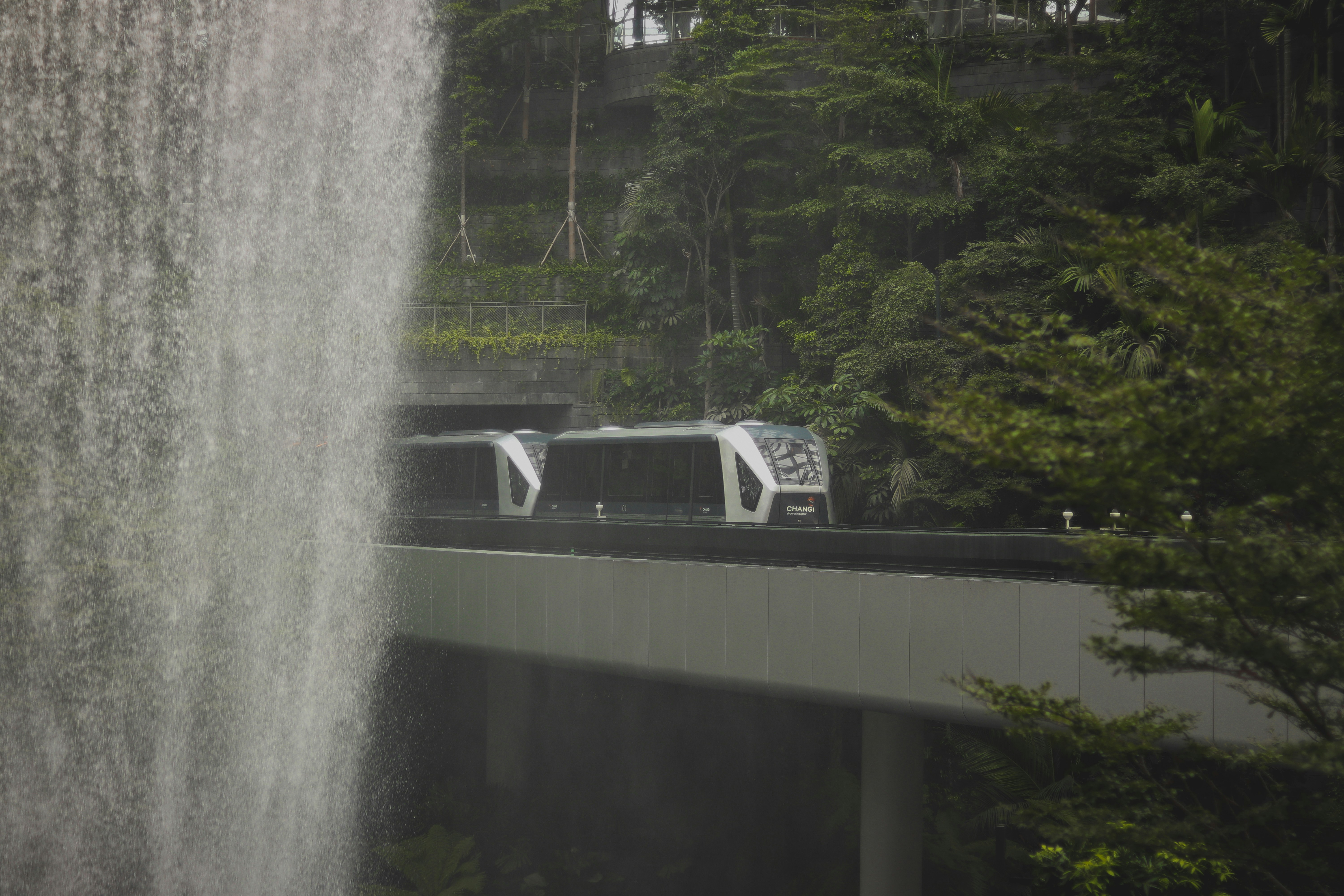 A modern train glides along a sleek track, framed by a majestic waterfall and lush greenery. The scene captures the harmony of nature and urban transit.