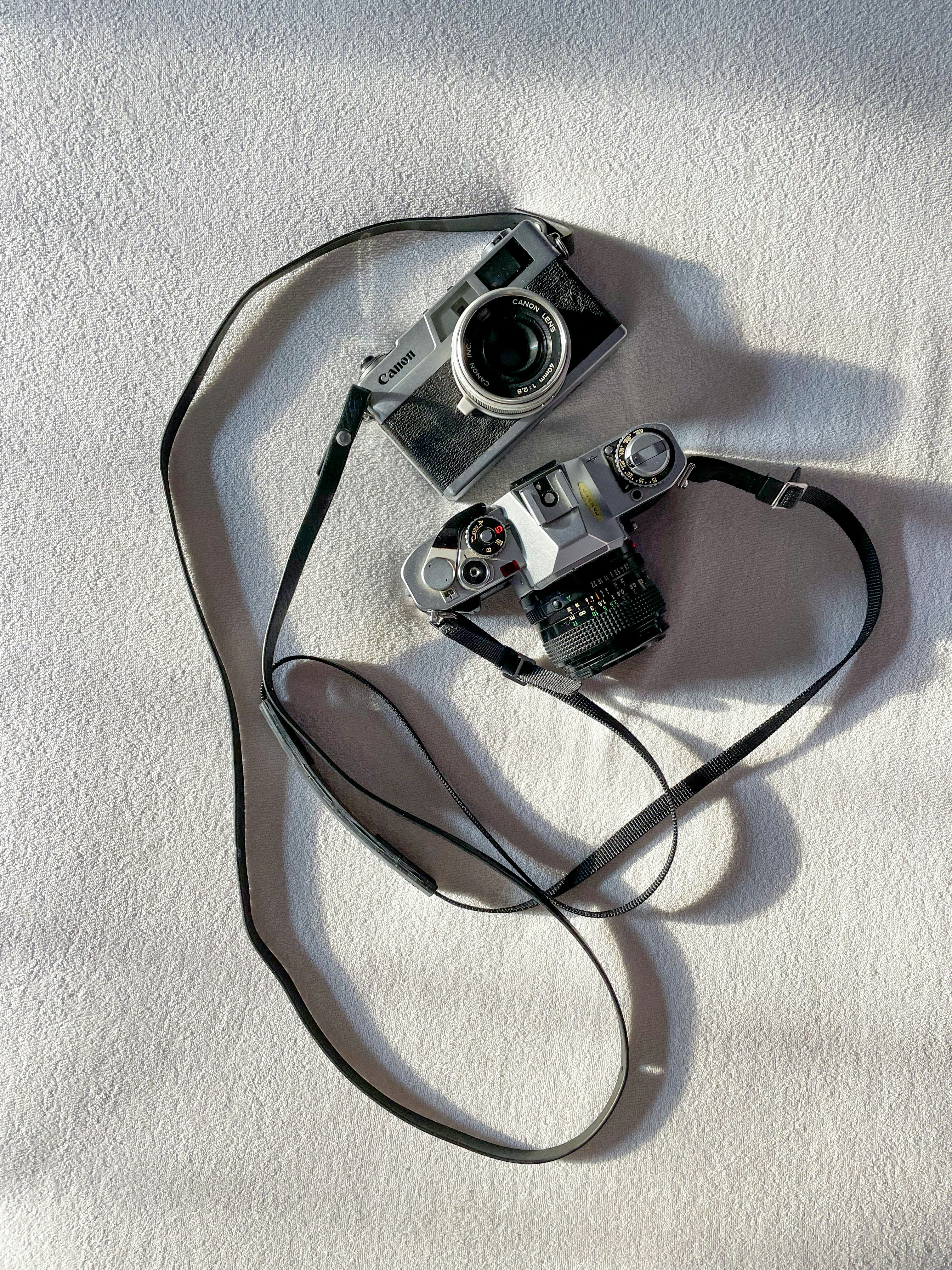 Two classic cameras with straps laid on a textured surface, showcasing their timeless design and craftsmanship.
