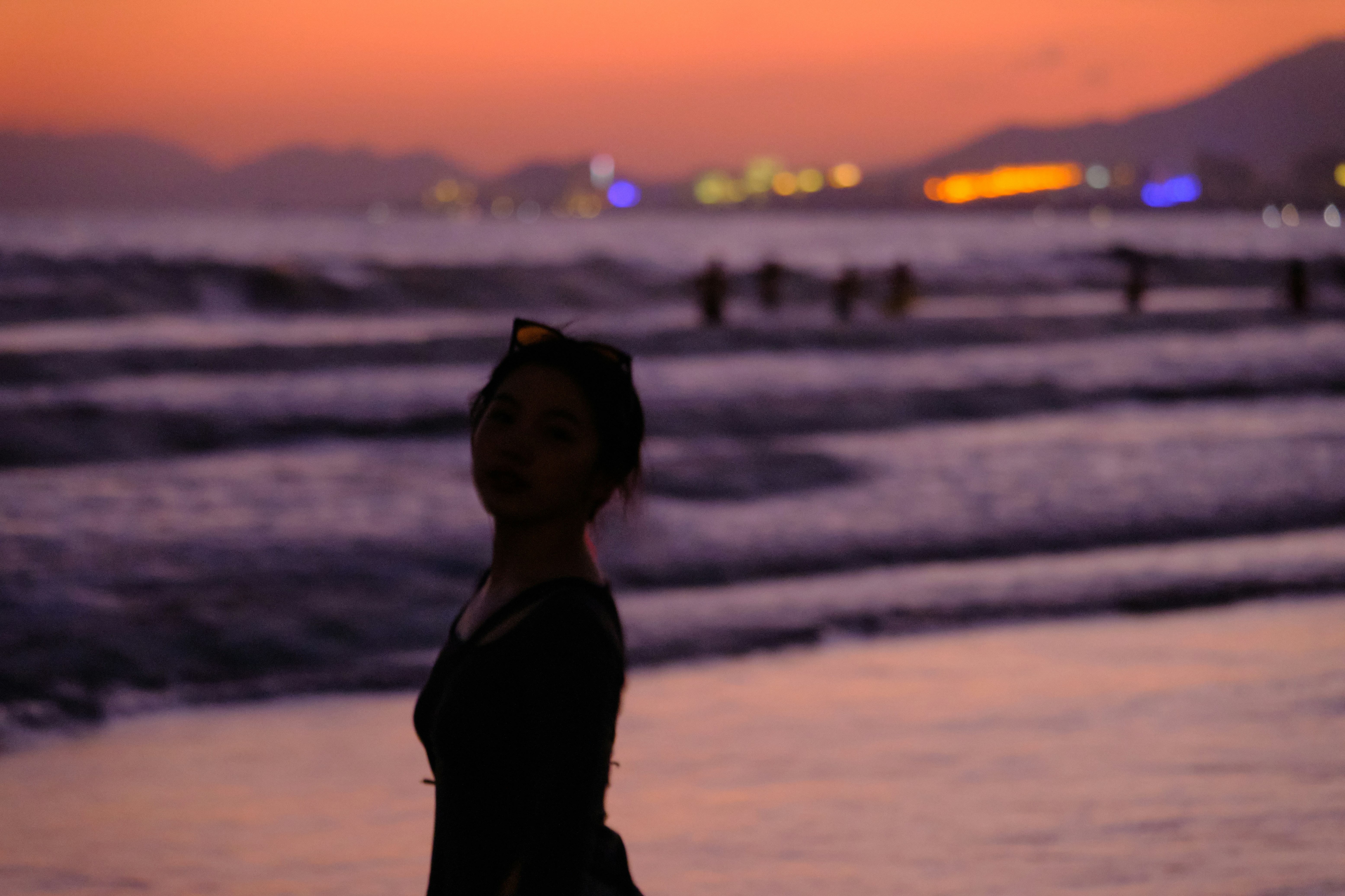 Silhouette at Dusk: Beach Portrait with Distant Neon Harbor Glow