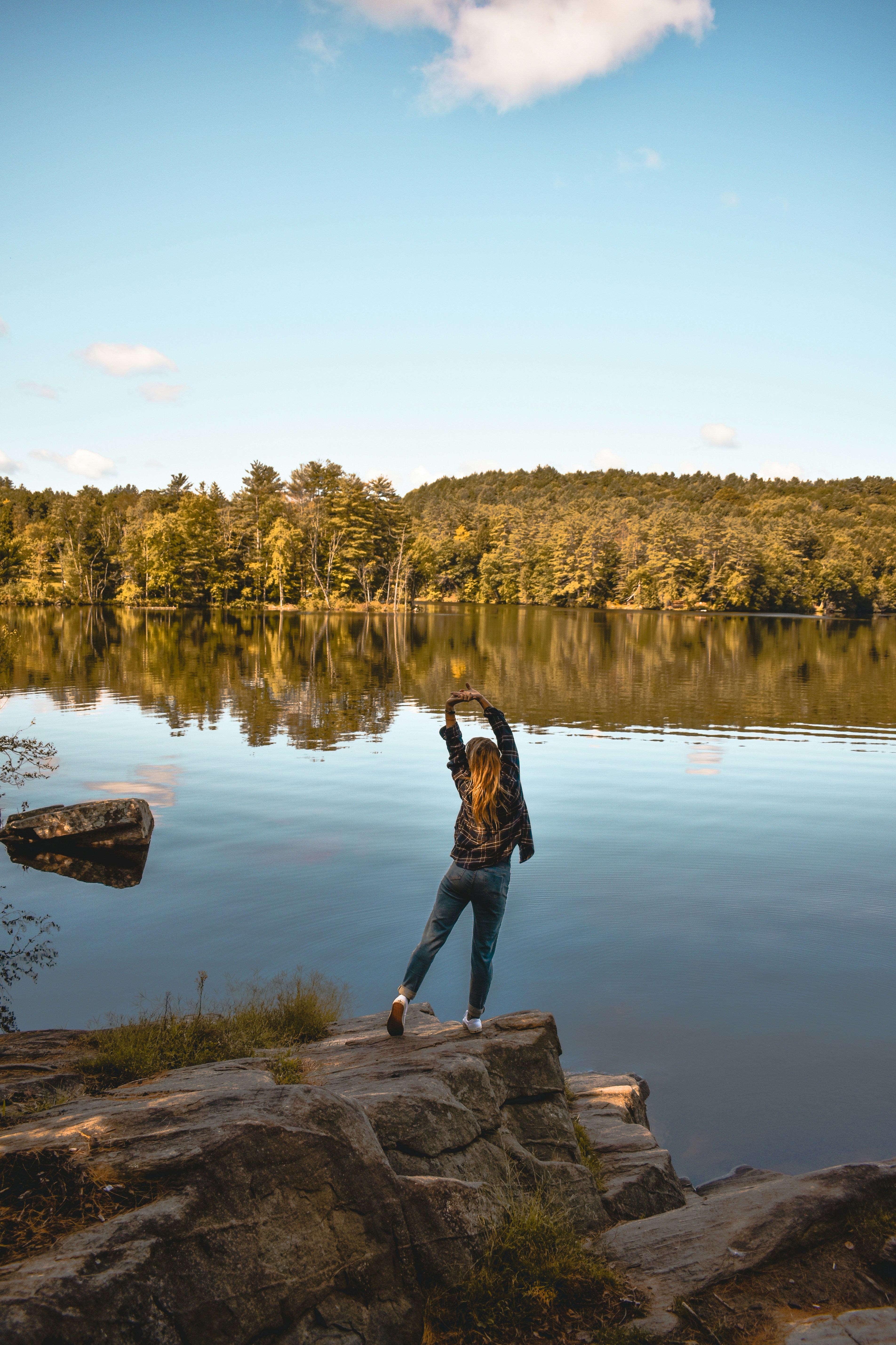 A person standing on rocky terrain, capturing the tranquil lake and surrounding trees in the golden hour light.