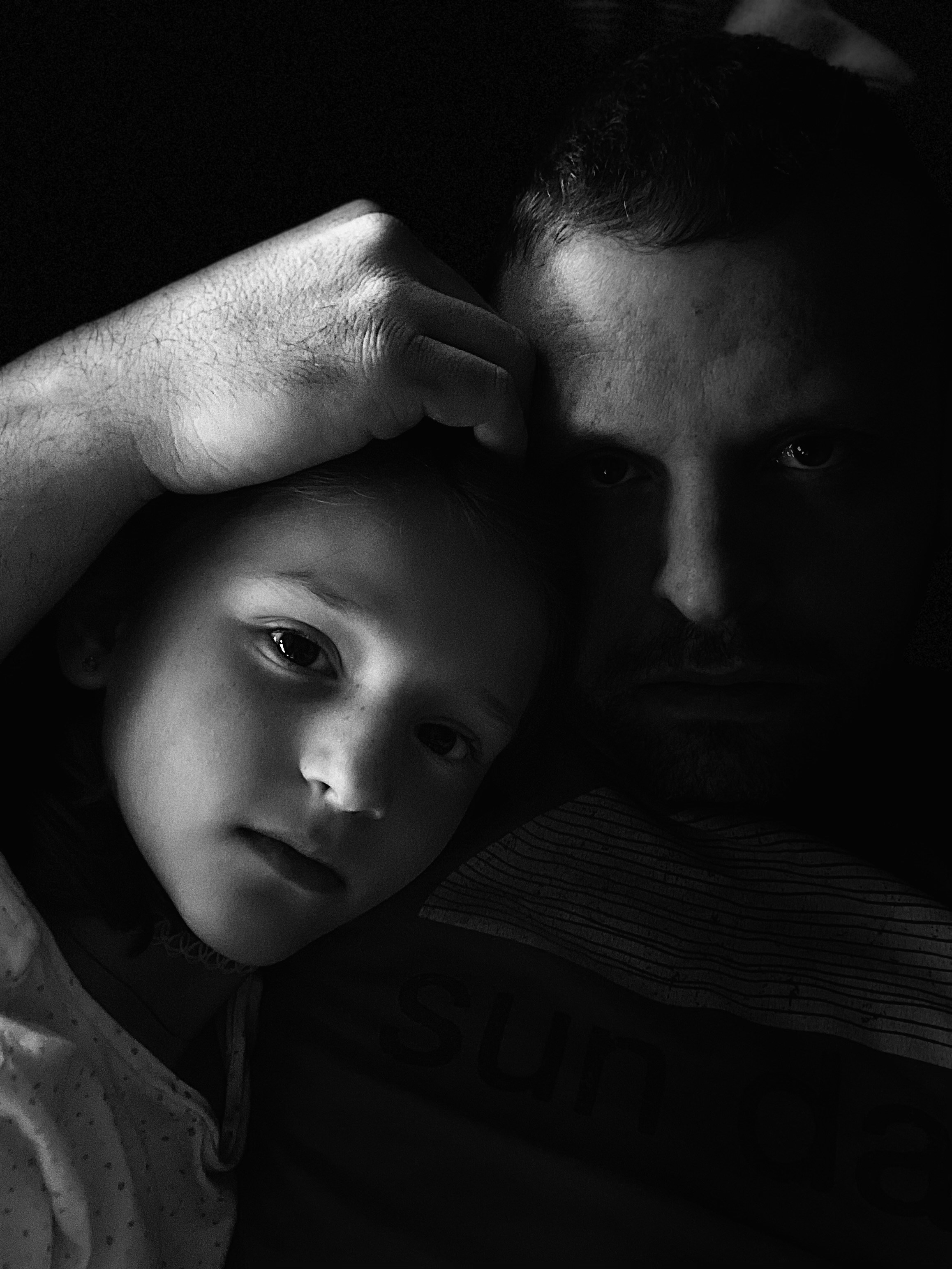 Father and child share a quiet embrace in dramatic black and white lighting.