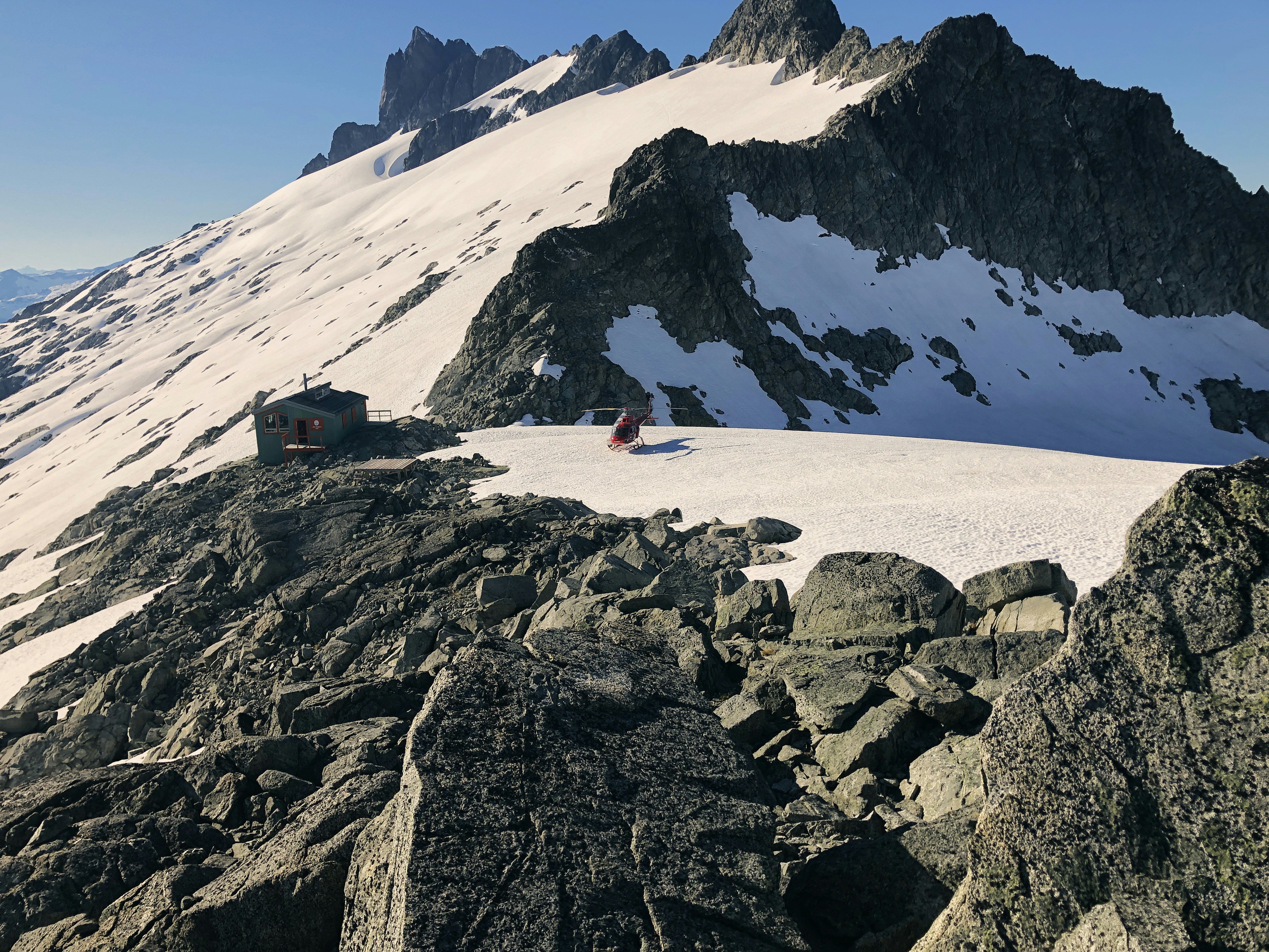 Red-clad figure traces a sunlit alpine ridge beside a solitary hut