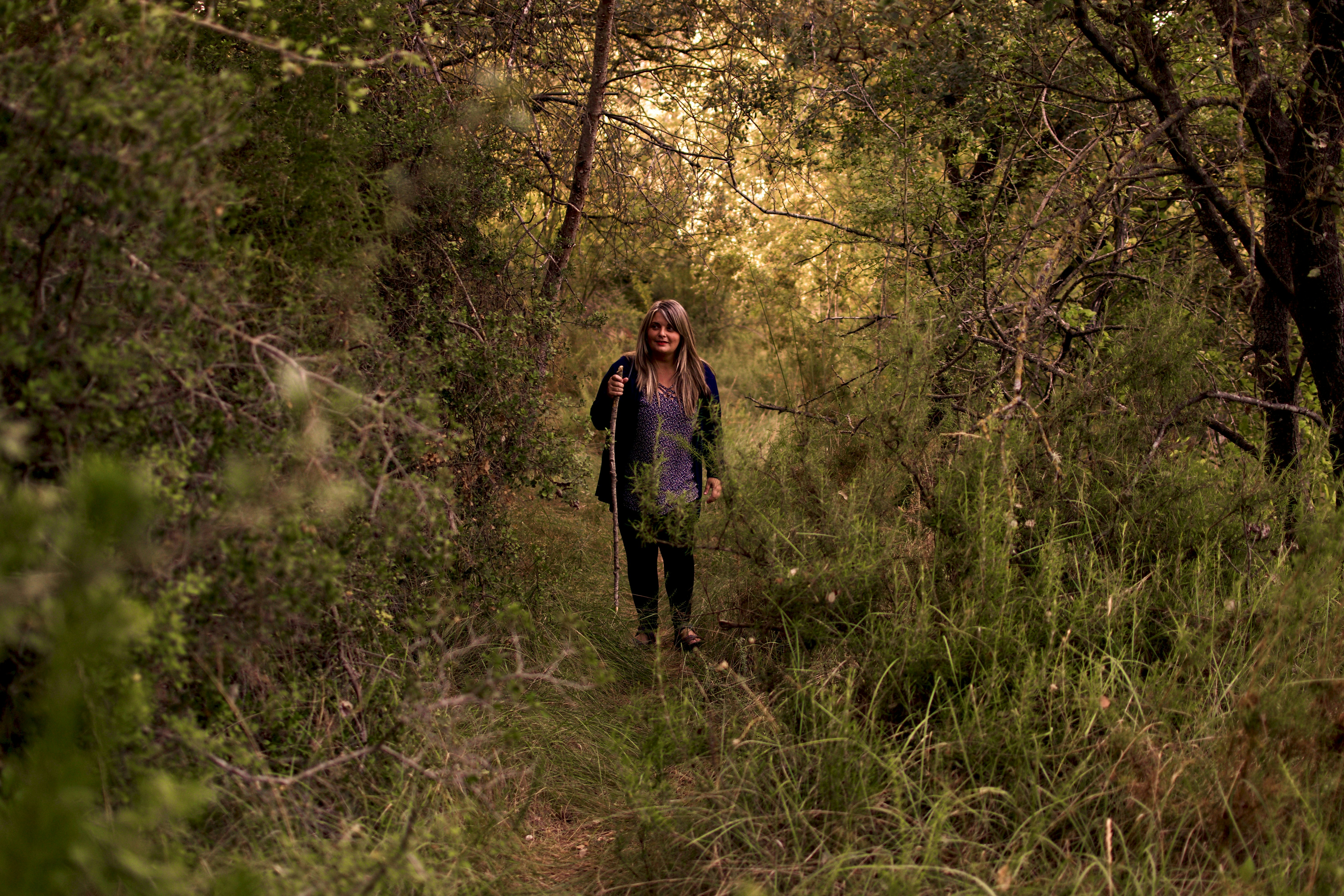 Hiker navigating a lush trail surrounded by dense foliage and dappled sunlight filtering through the trees.