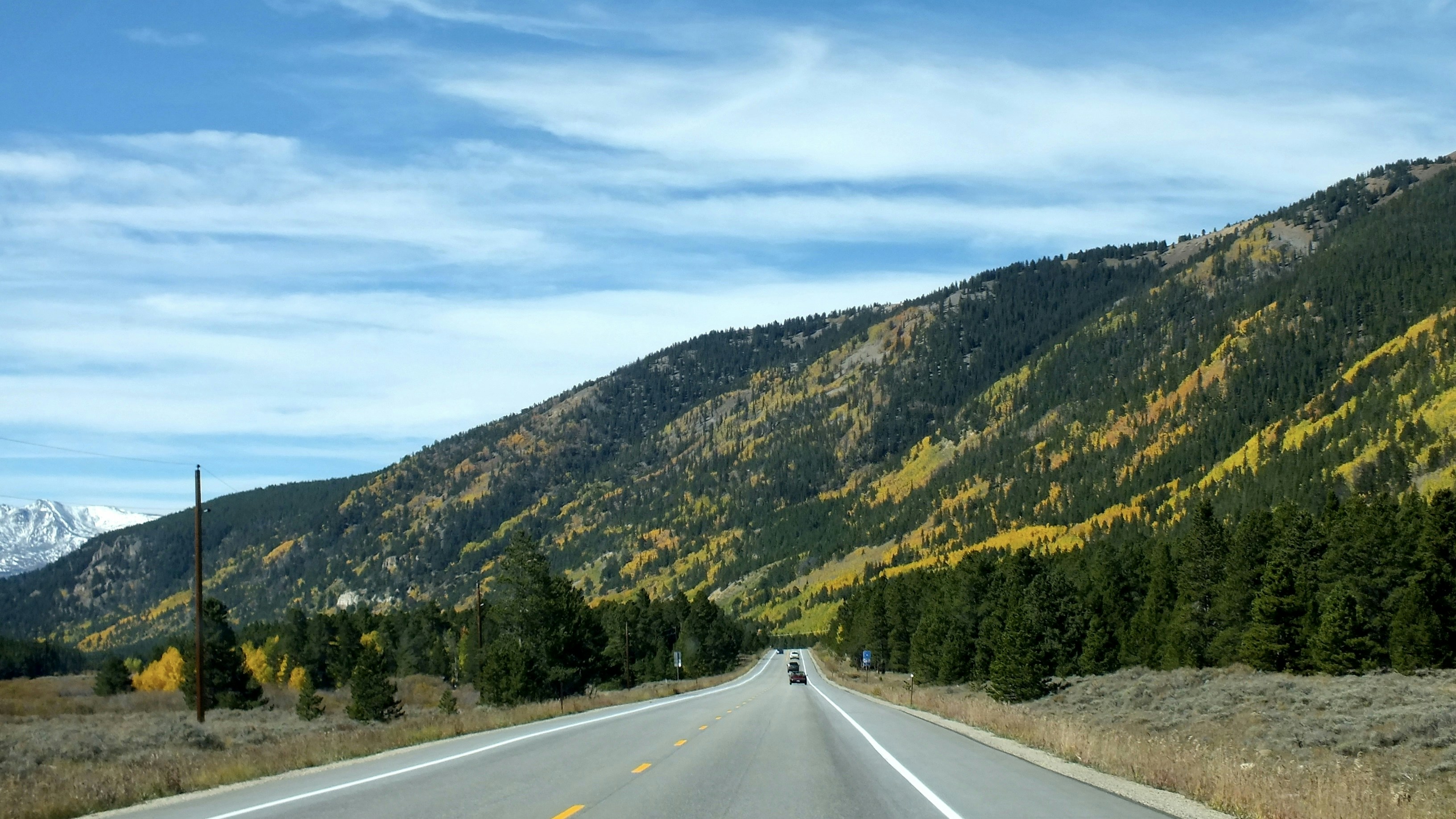 Autumn highway photograph showing a long straight road through golden foothills and pines under a bright blue sky, receding to a distant vanishing point.