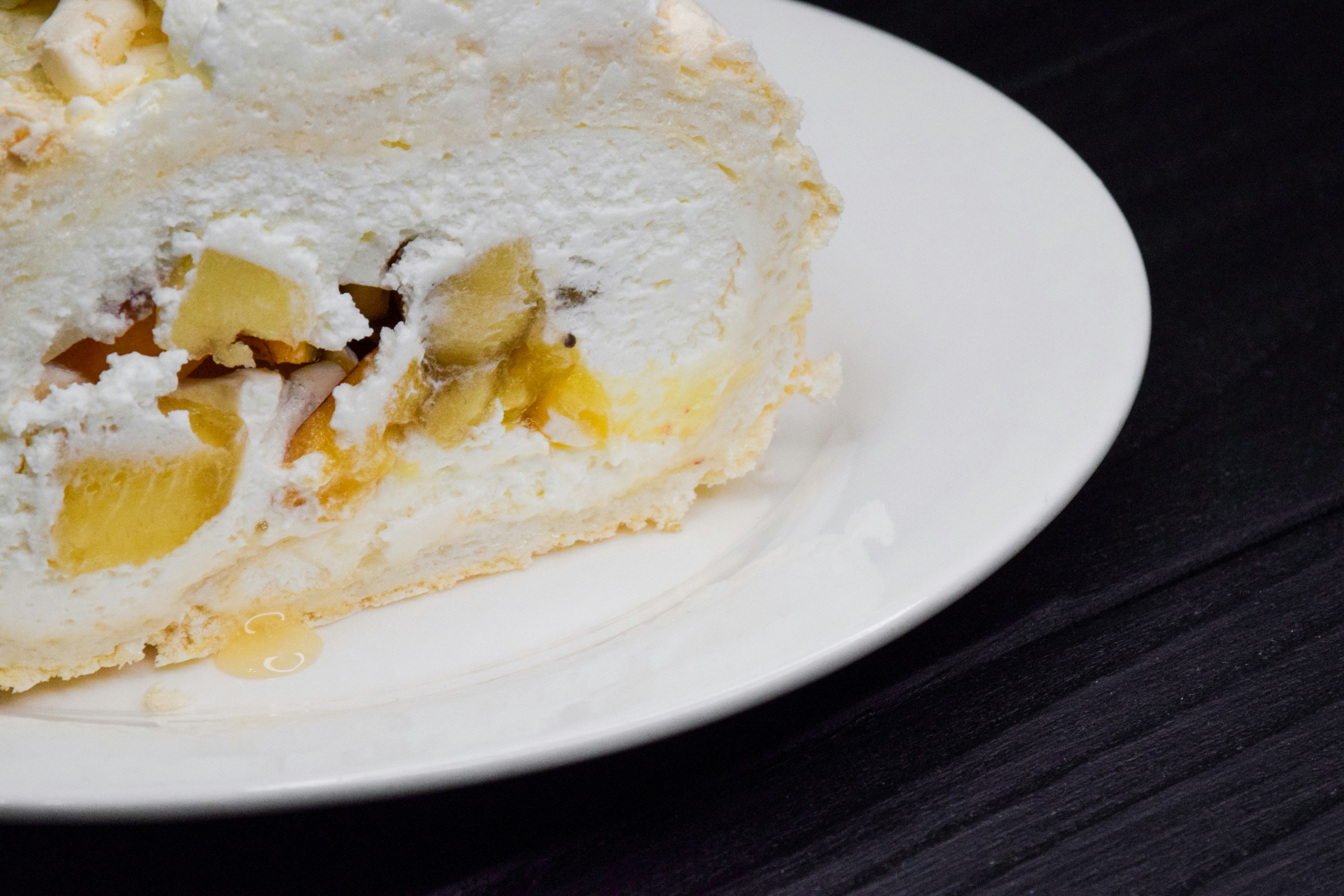 A slice of fruit-filled cake showcasing layers of whipped cream and tropical fruits on a white plate.