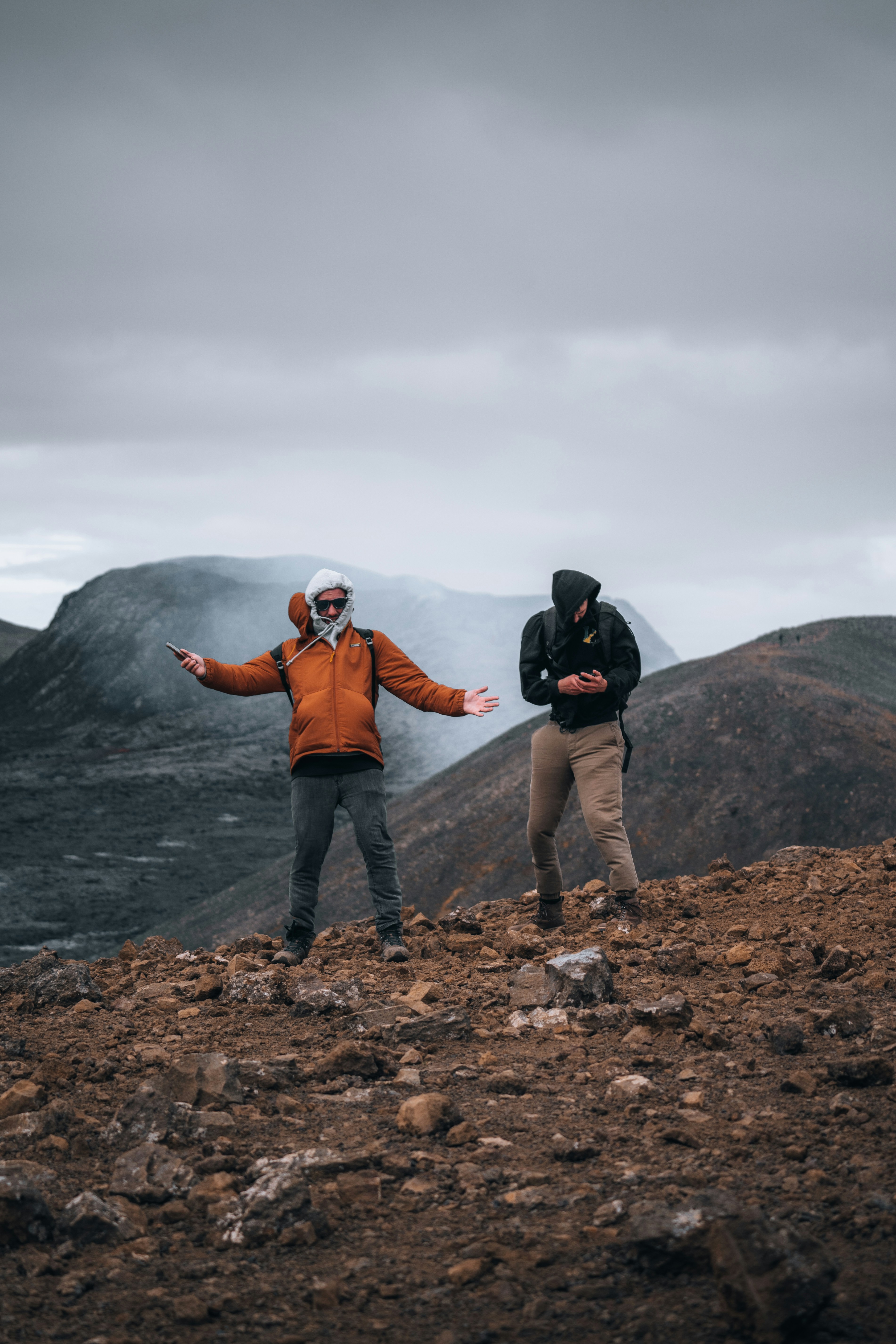 Two hikers celebrating their achievement on a rocky mountain terrain under a moody sky. The rugged landscape emphasizes their adventurous spirit.