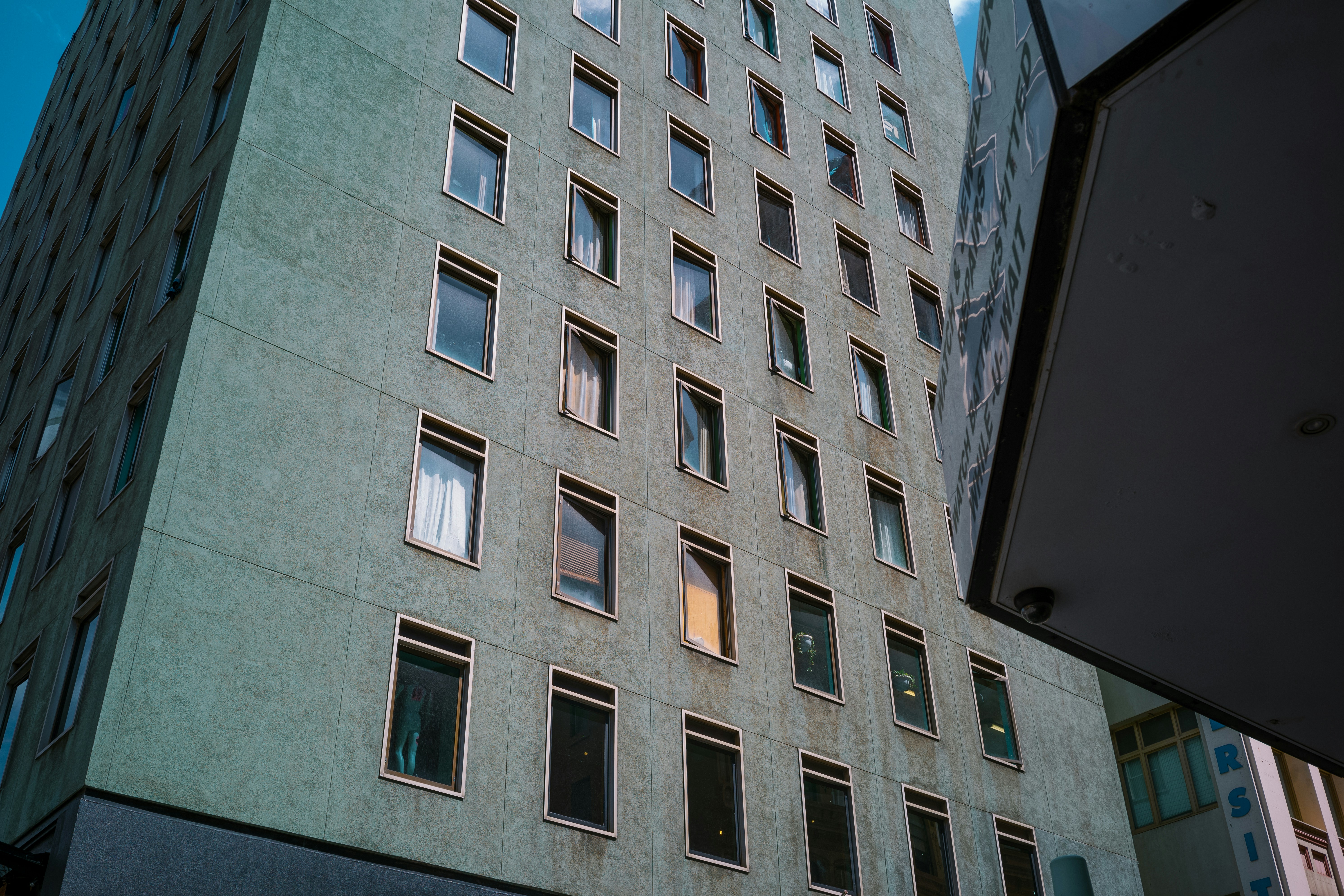 Modern building facade showcasing a grid of windows reflecting ambient light, with a hint of urban life peeking through.