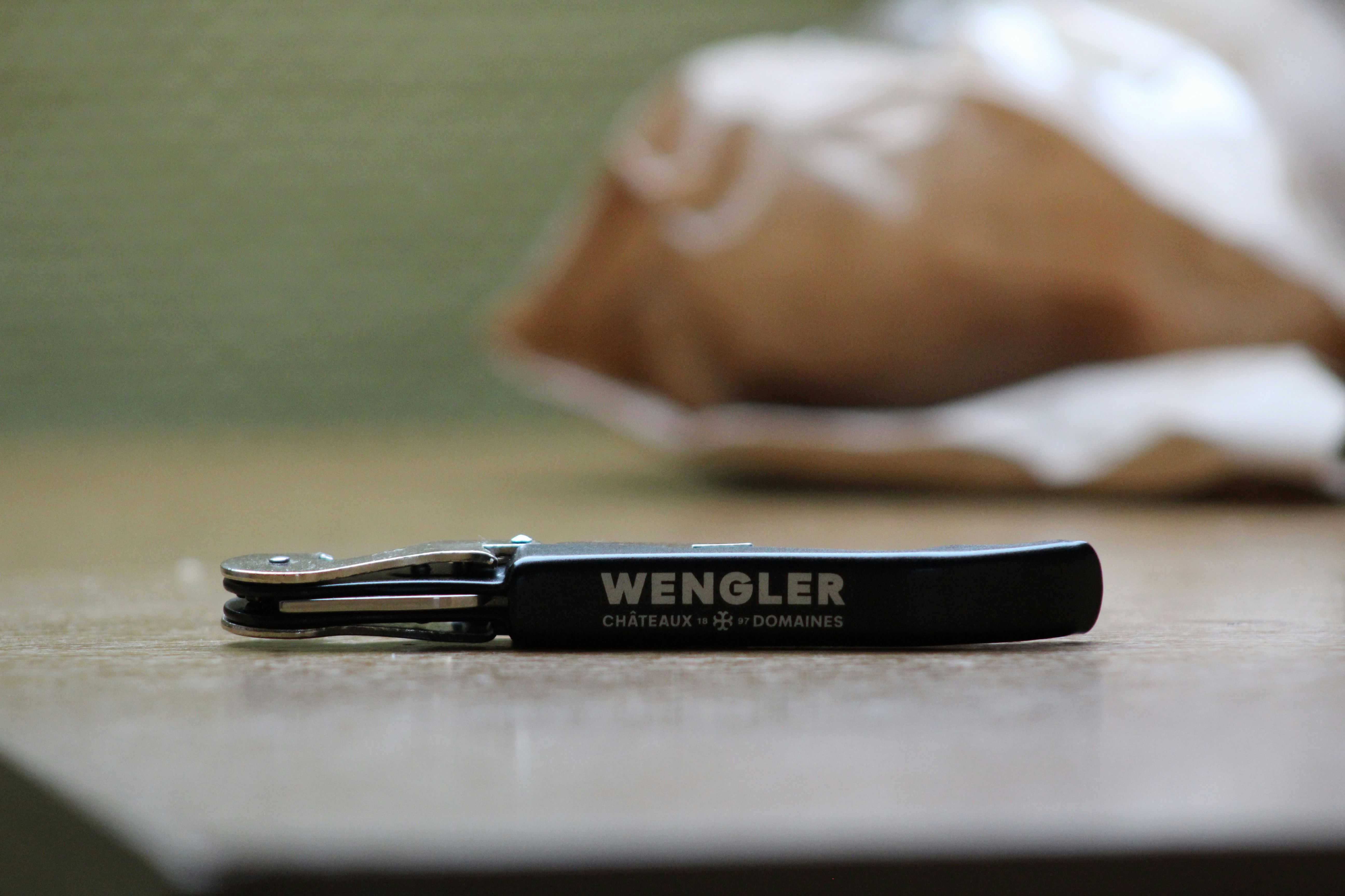 Close-up of a branded corkscrew resting on a wooden table, with a blurred background that hints at a casual dining setting.