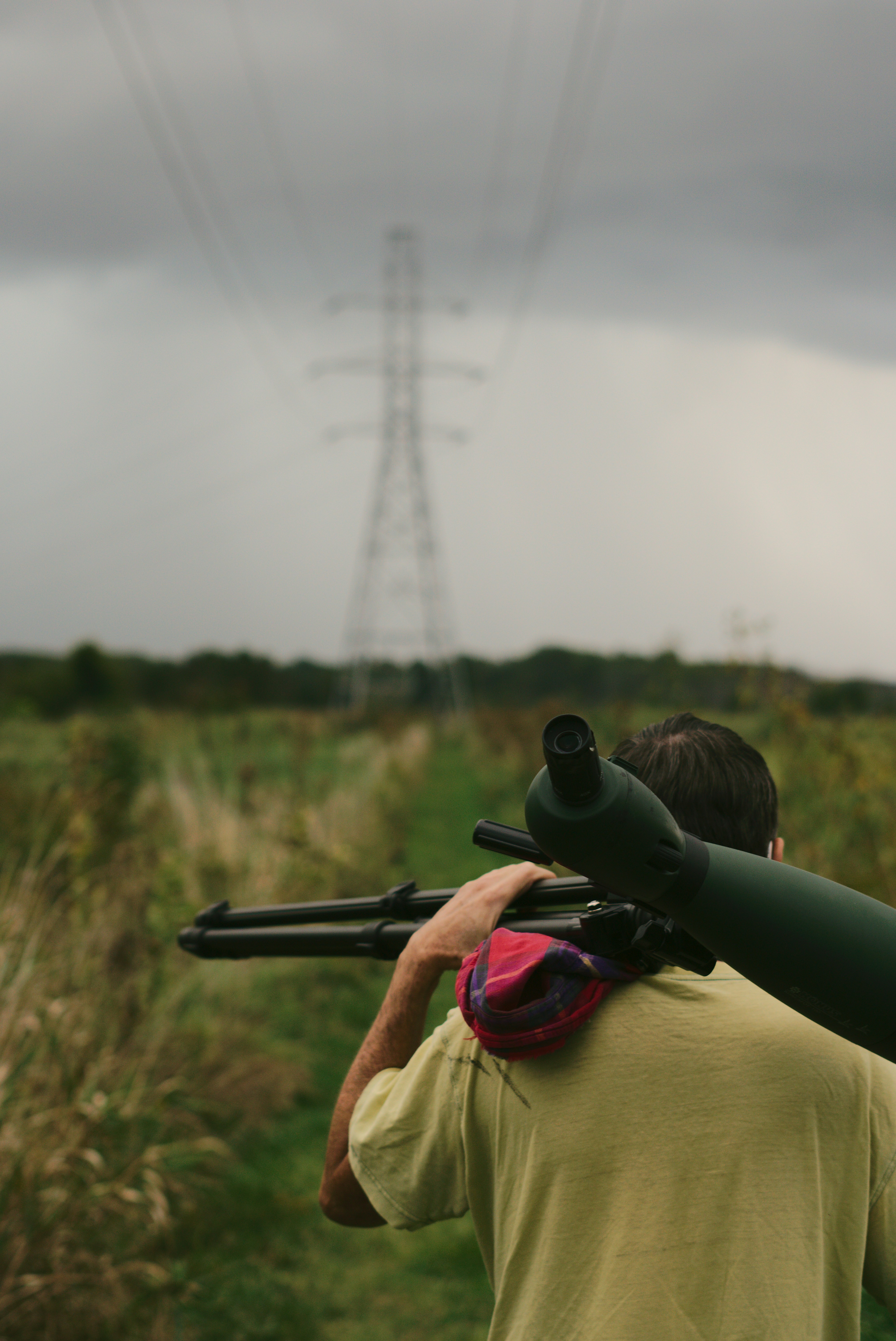 Moody Horizon: Hunter Carries a Rifle Toward a Distant Transmission Tower