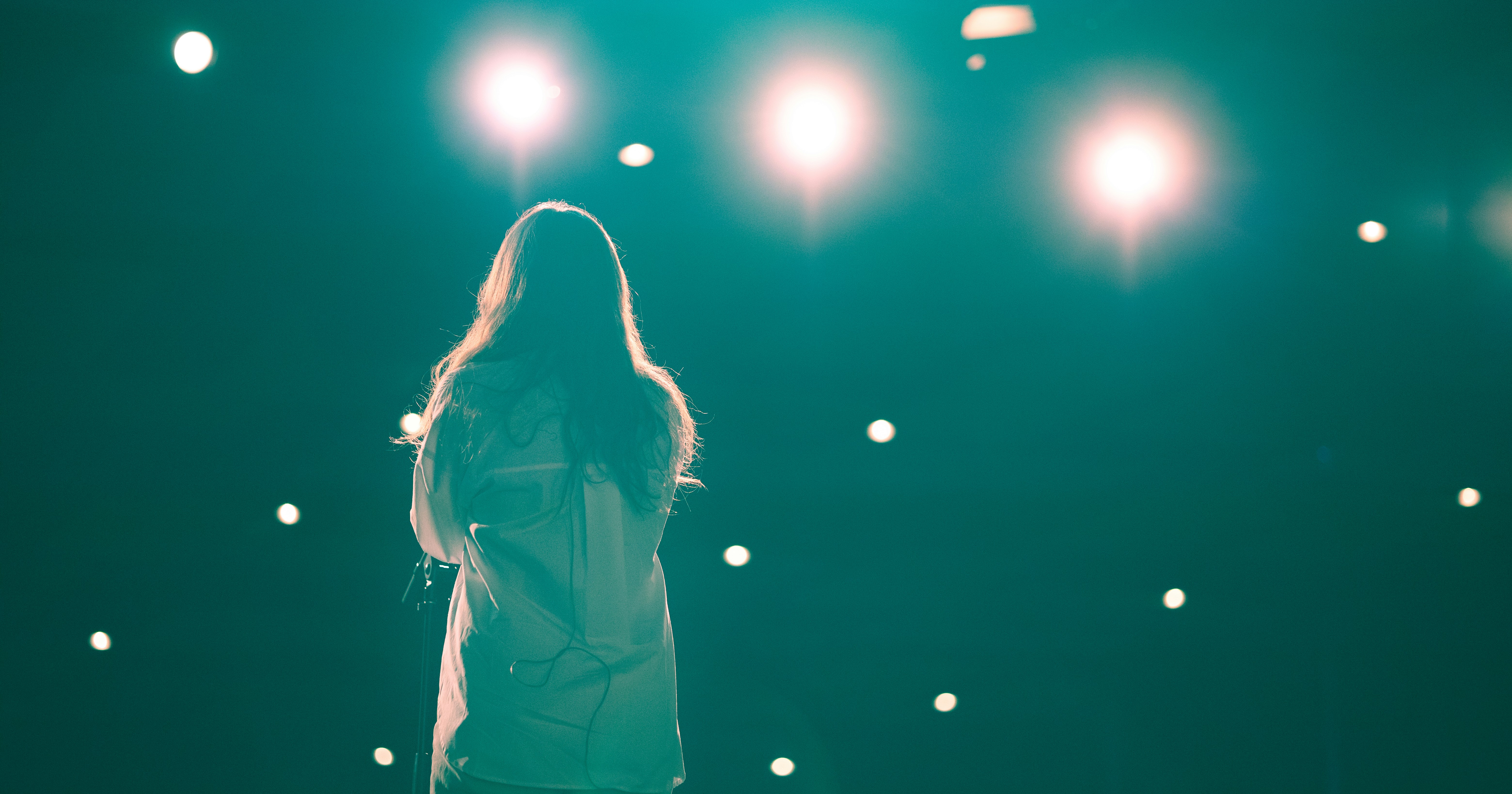 Silhouette of a woman standing under vibrant green lights on a stage.