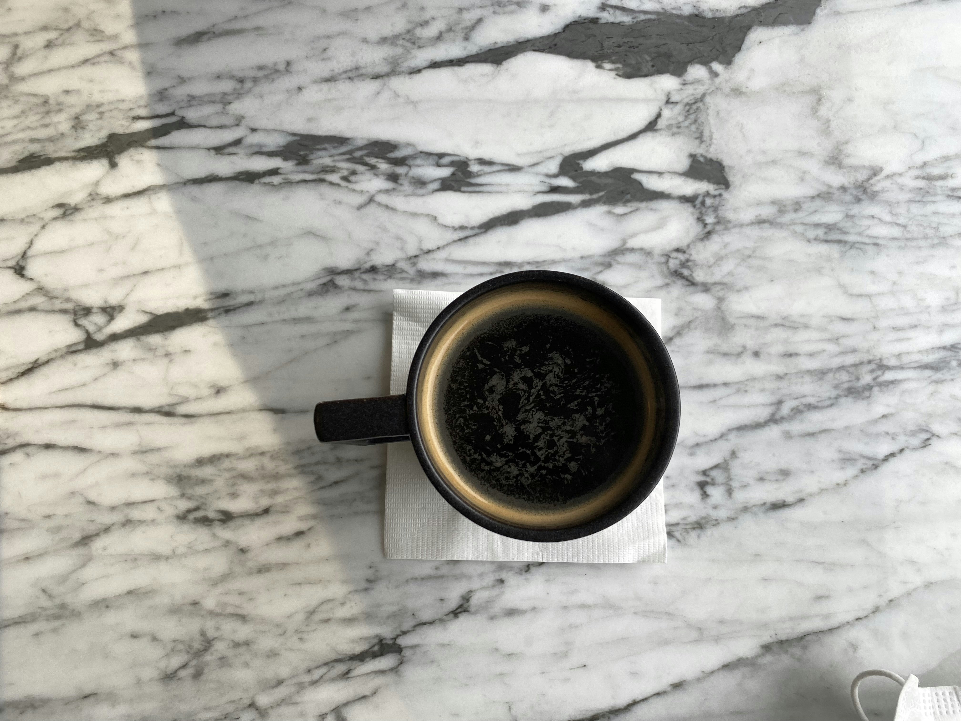 A black coffee cup resting on a white napkin atop a marble table, showcasing intricate patterns of the stone. The scene evokes a tranquil atmosphere perfect for reflection.