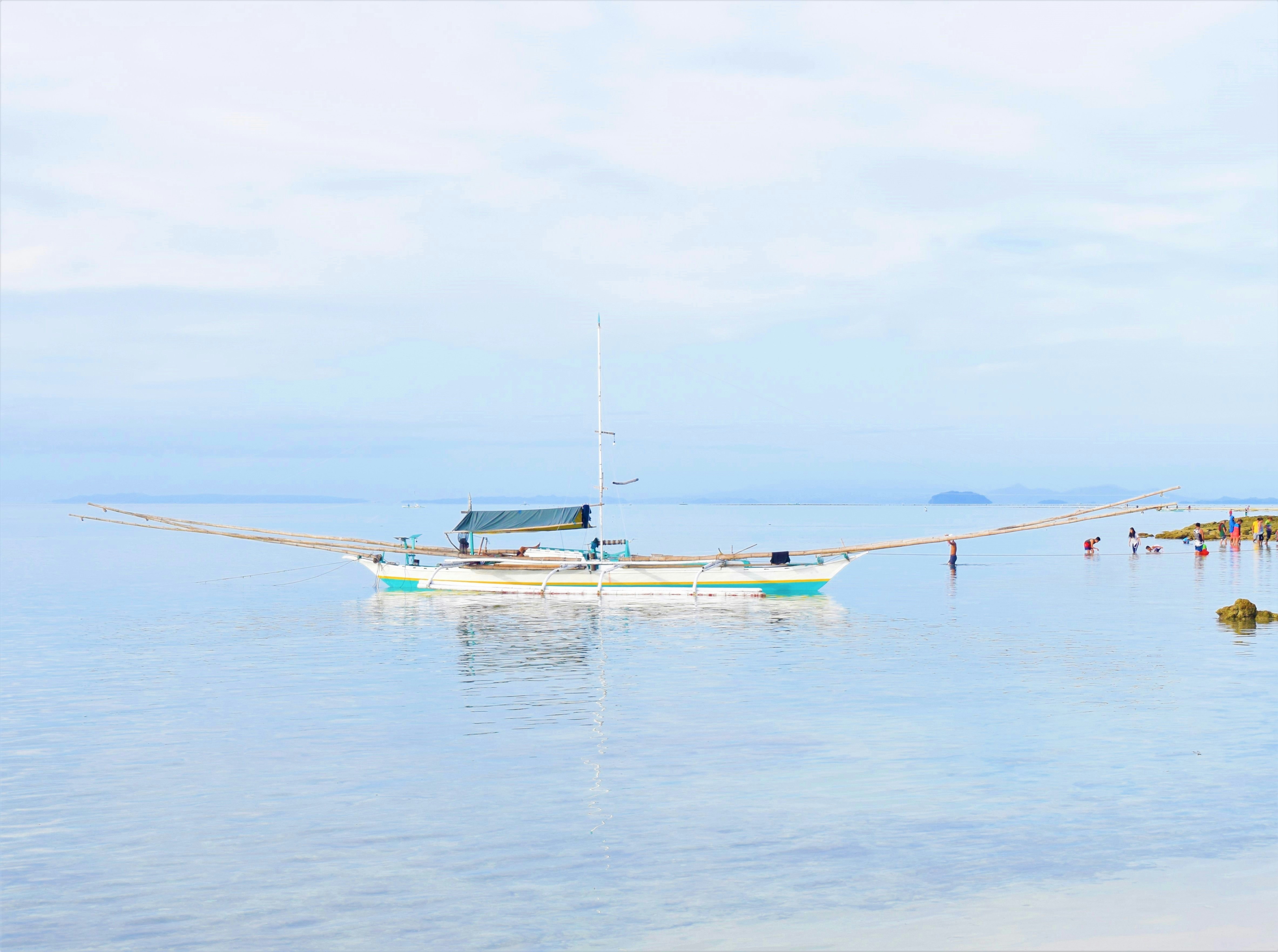 Traditional boat anchored on calm waters, reflecting the serene sky. The scene captures a tranquil moment in a coastal setting.