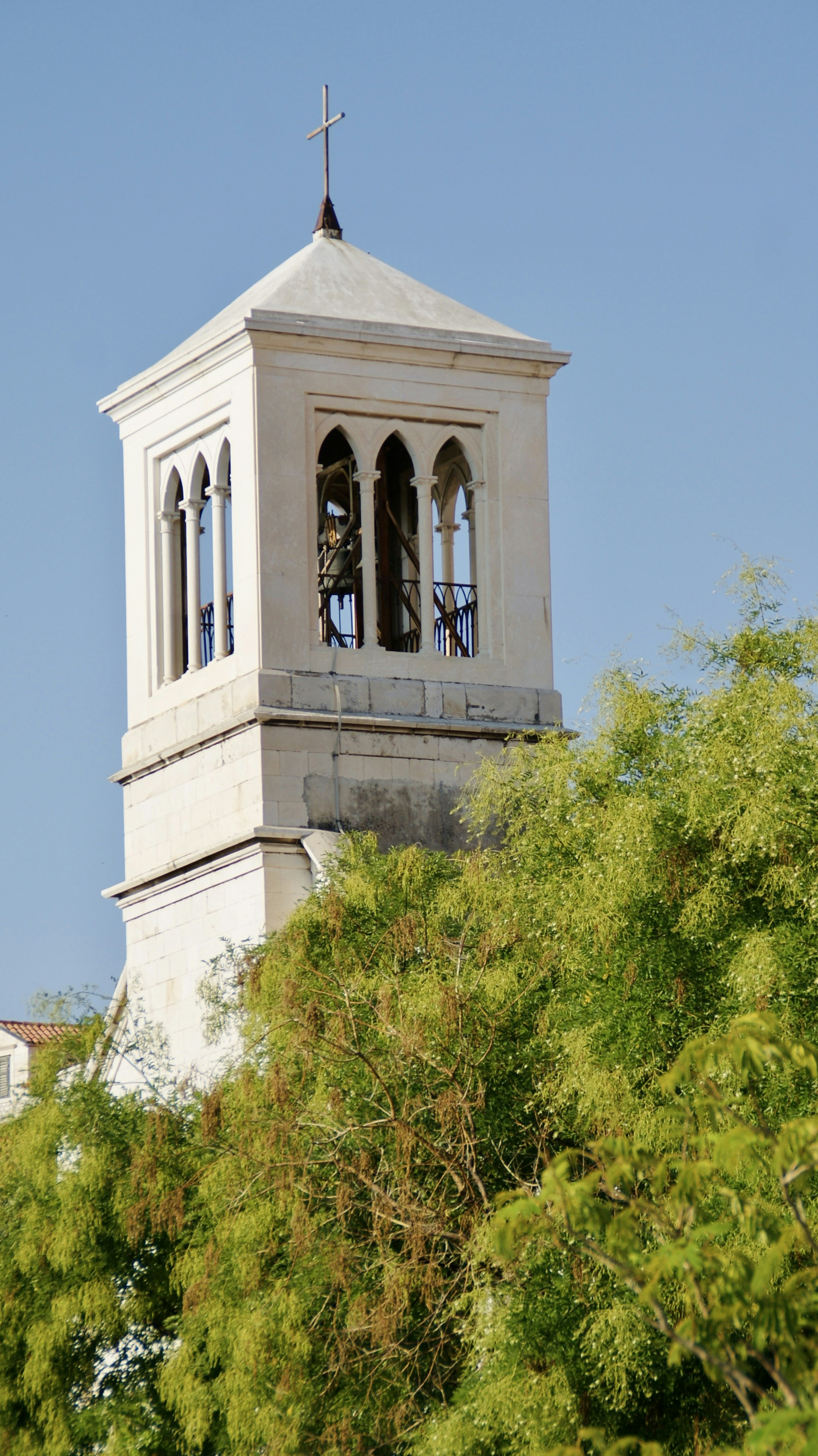 Bell tower adorned with a cross, partially obscured by lush greenery. The architectural details highlight its historical significance.