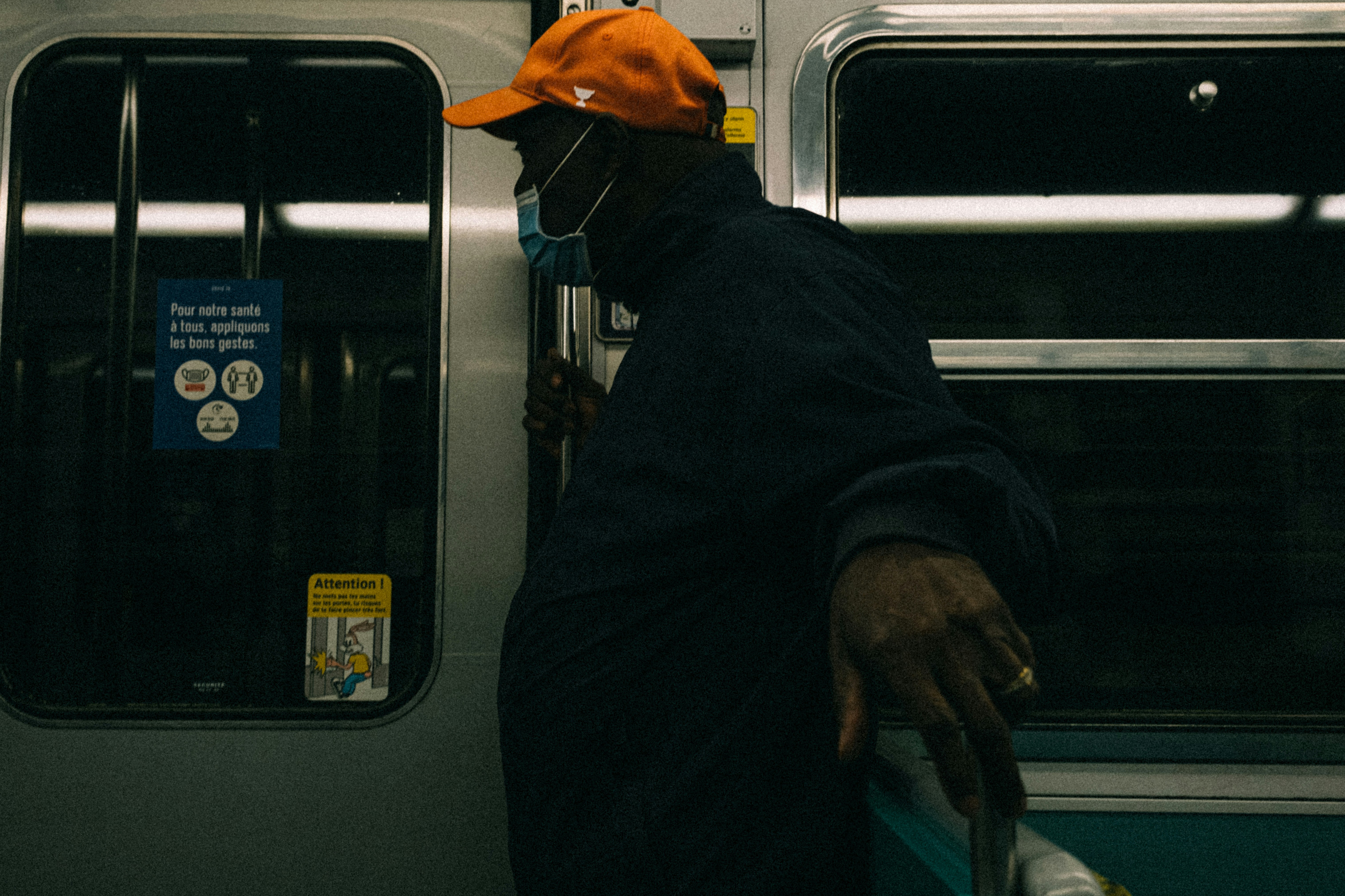 Orange Cap at the Threshold of a Dim Subway Car