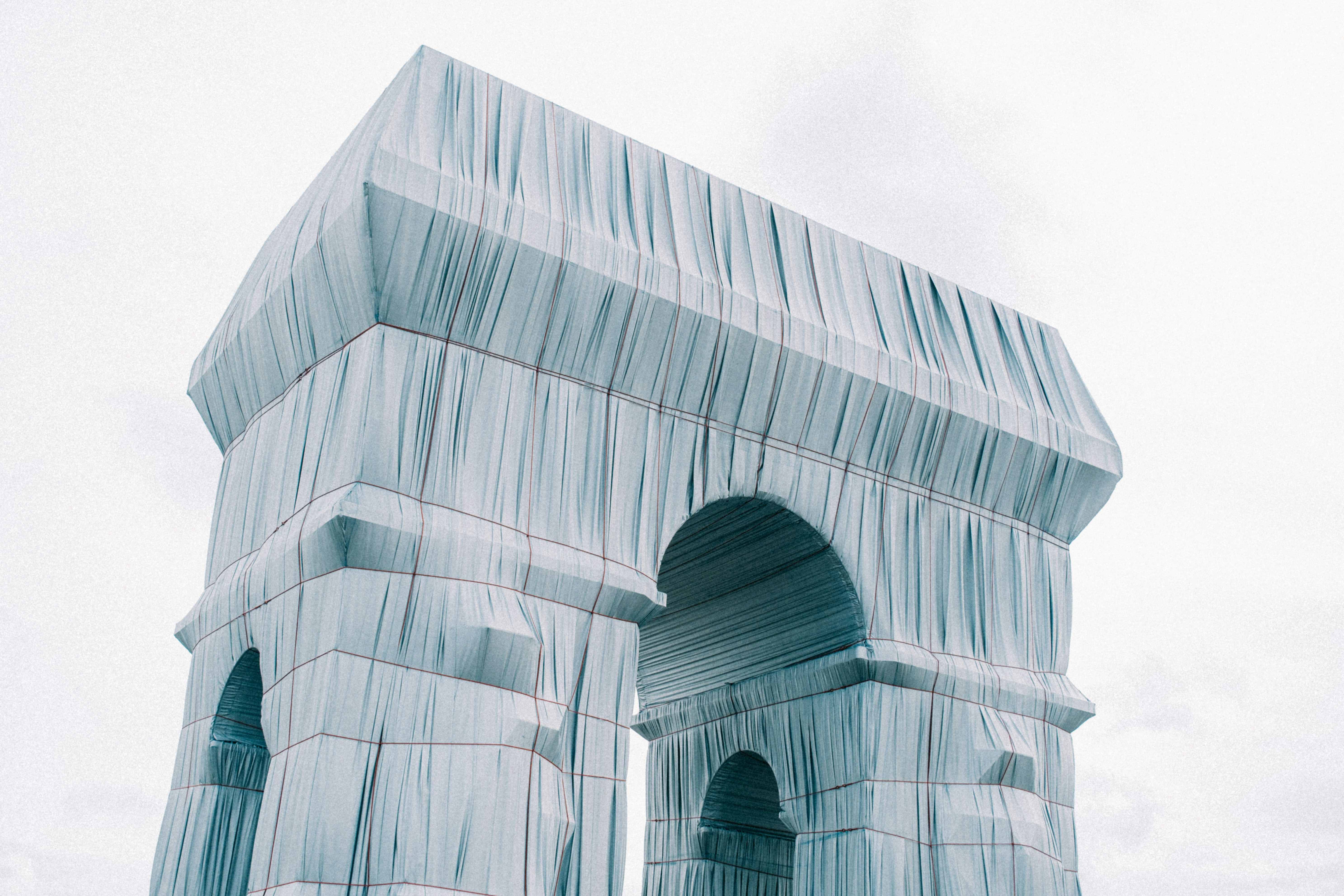 A large archway wrapped in flowing fabric, showcasing a blend of contemporary art and architectural form. The soft, muted colors enhance the ethereal quality of the installation.