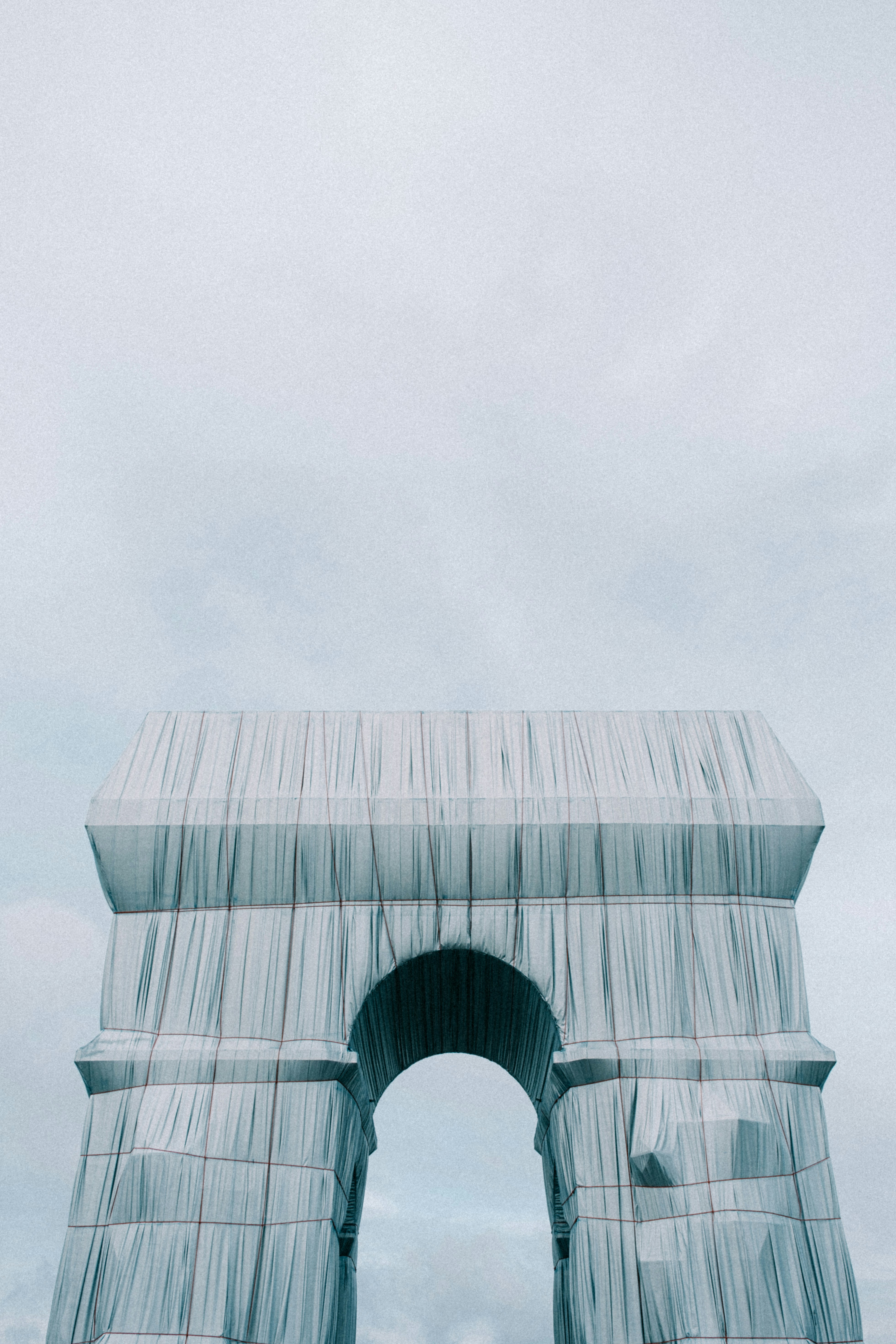 A monumental arch draped in translucent fabric, creating an ethereal effect against a cloudy sky.