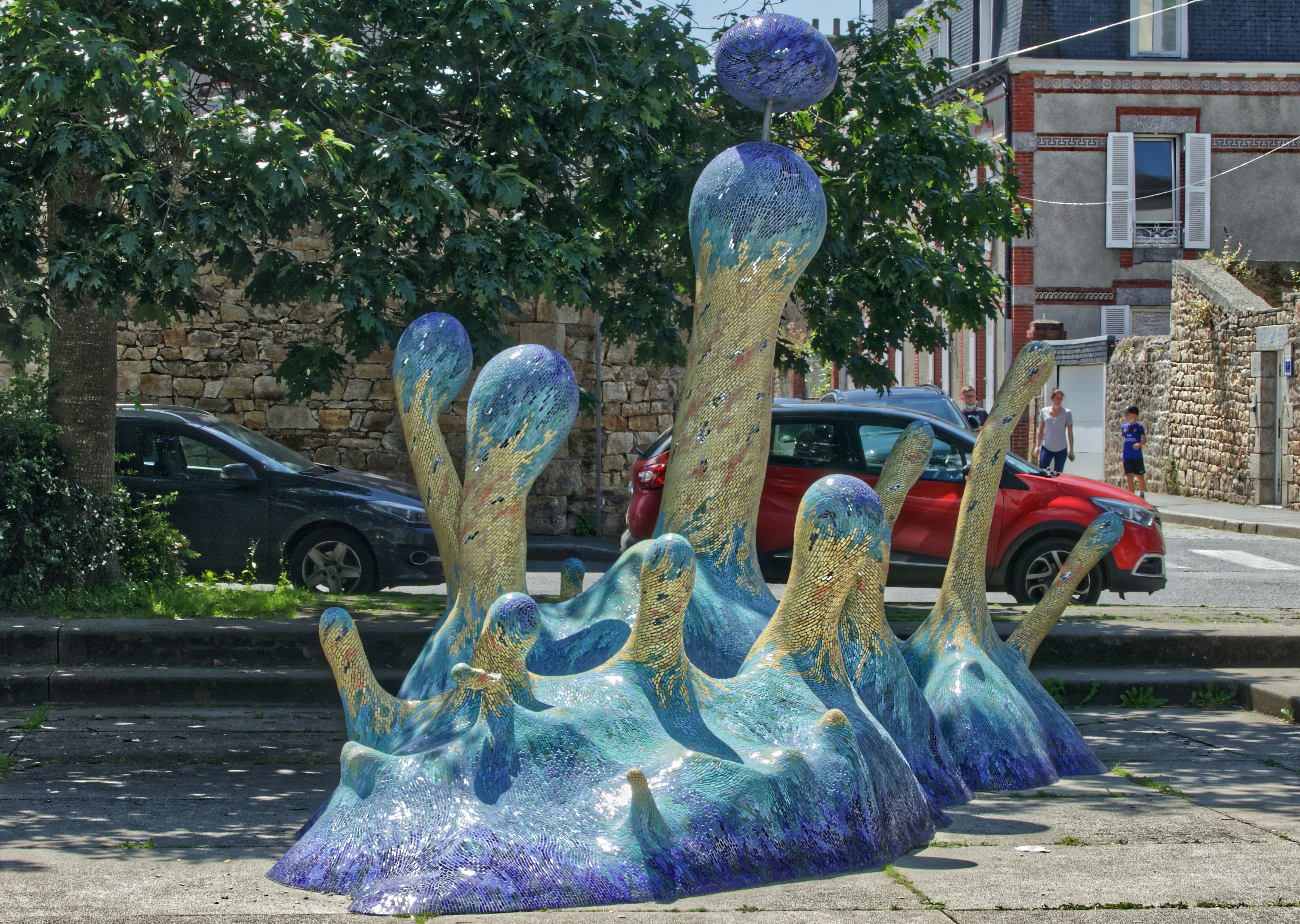 Colorful abstract sculpture resembling ocean waves, with vibrant textures and shapes, set against a tranquil urban backdrop.