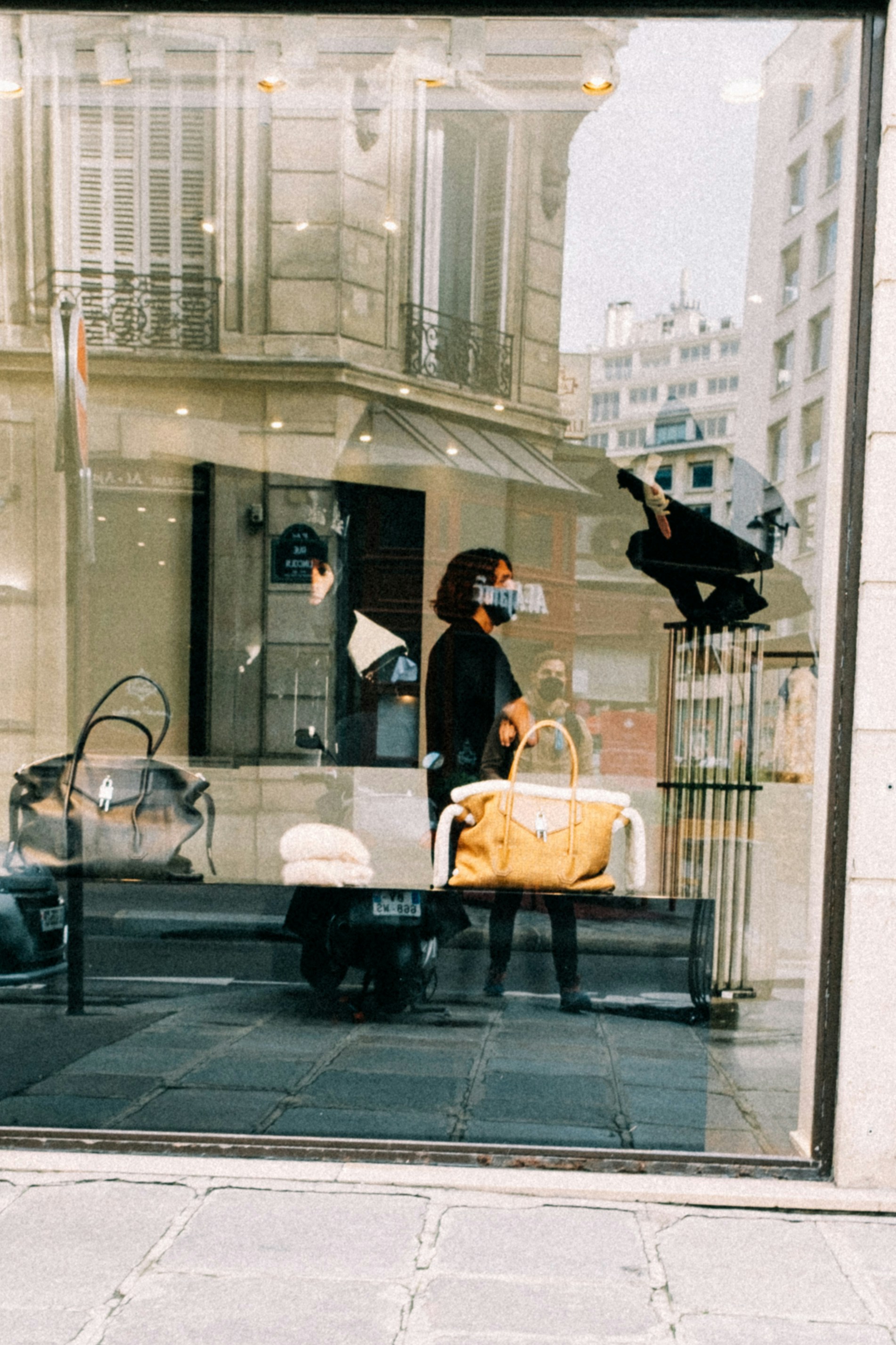 Reflected Portrait: A Masked Figure and a Tan Bag in the Shopfront Window