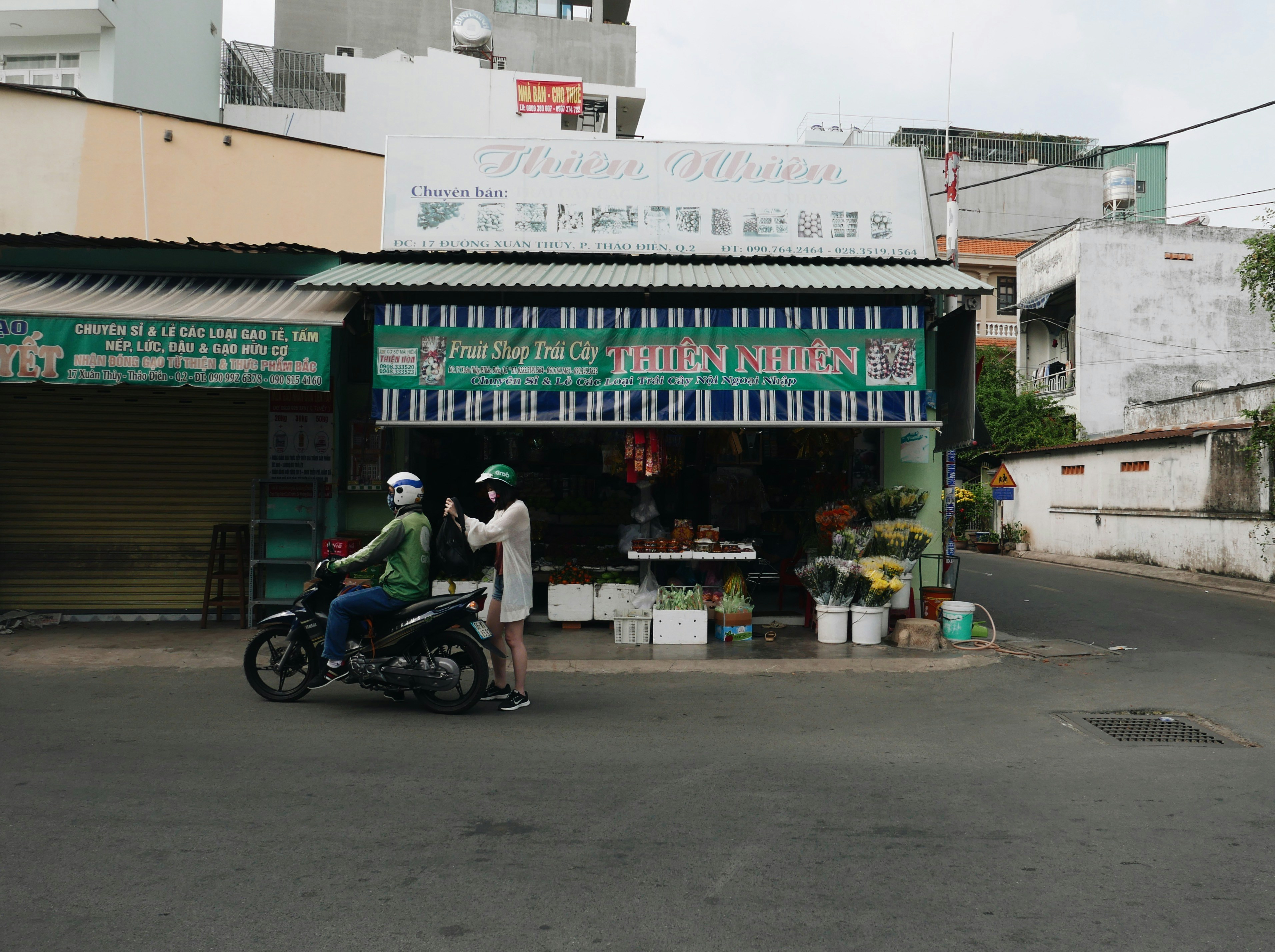 A vibrant fruit shop adorned with fresh produce and local goods, situated on a bustling street corner. The scene captures the essence of everyday life in a city.
