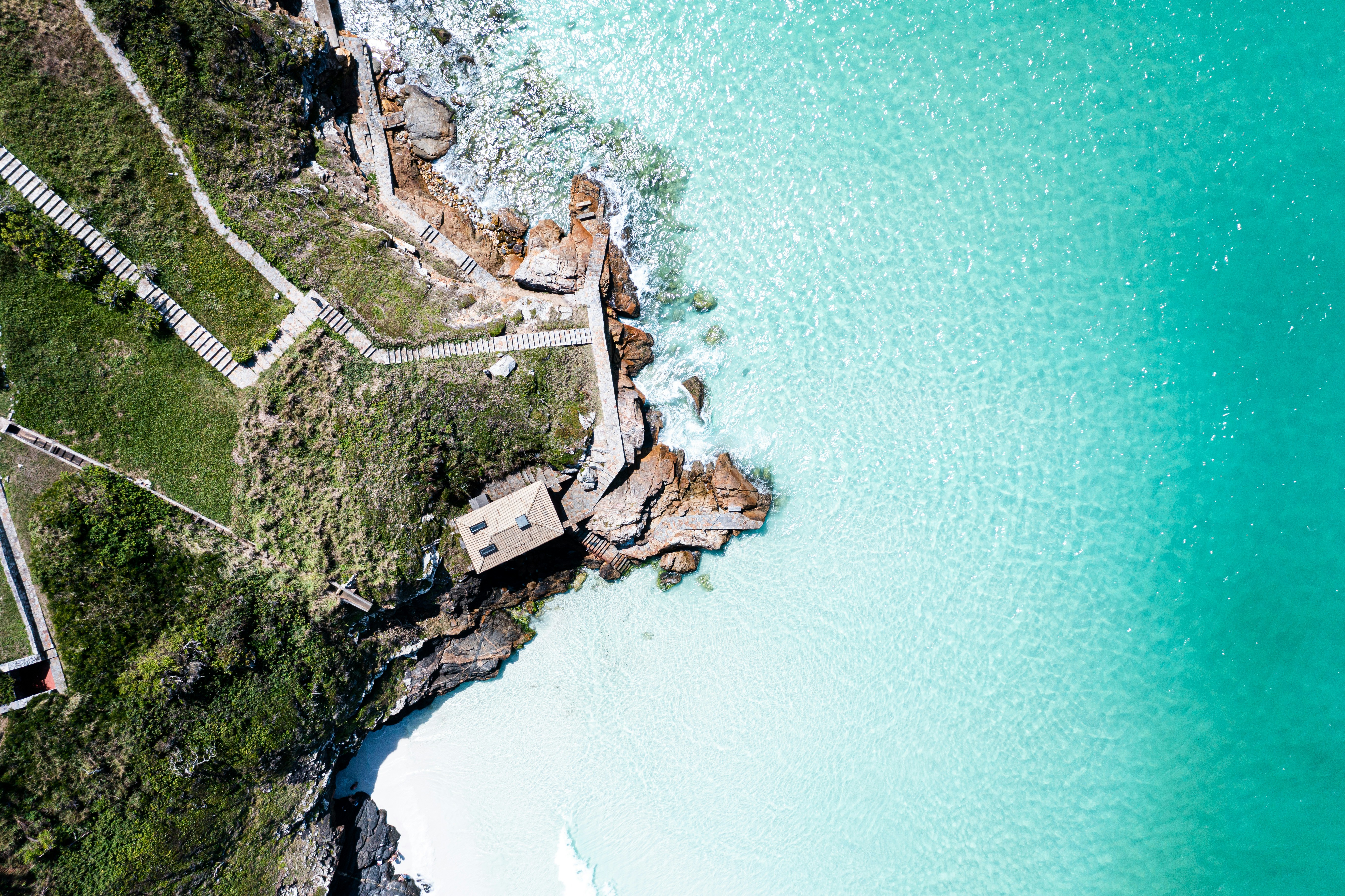 Aerial view of winding paths along a rocky coastline beside vibrant turquoise waters.