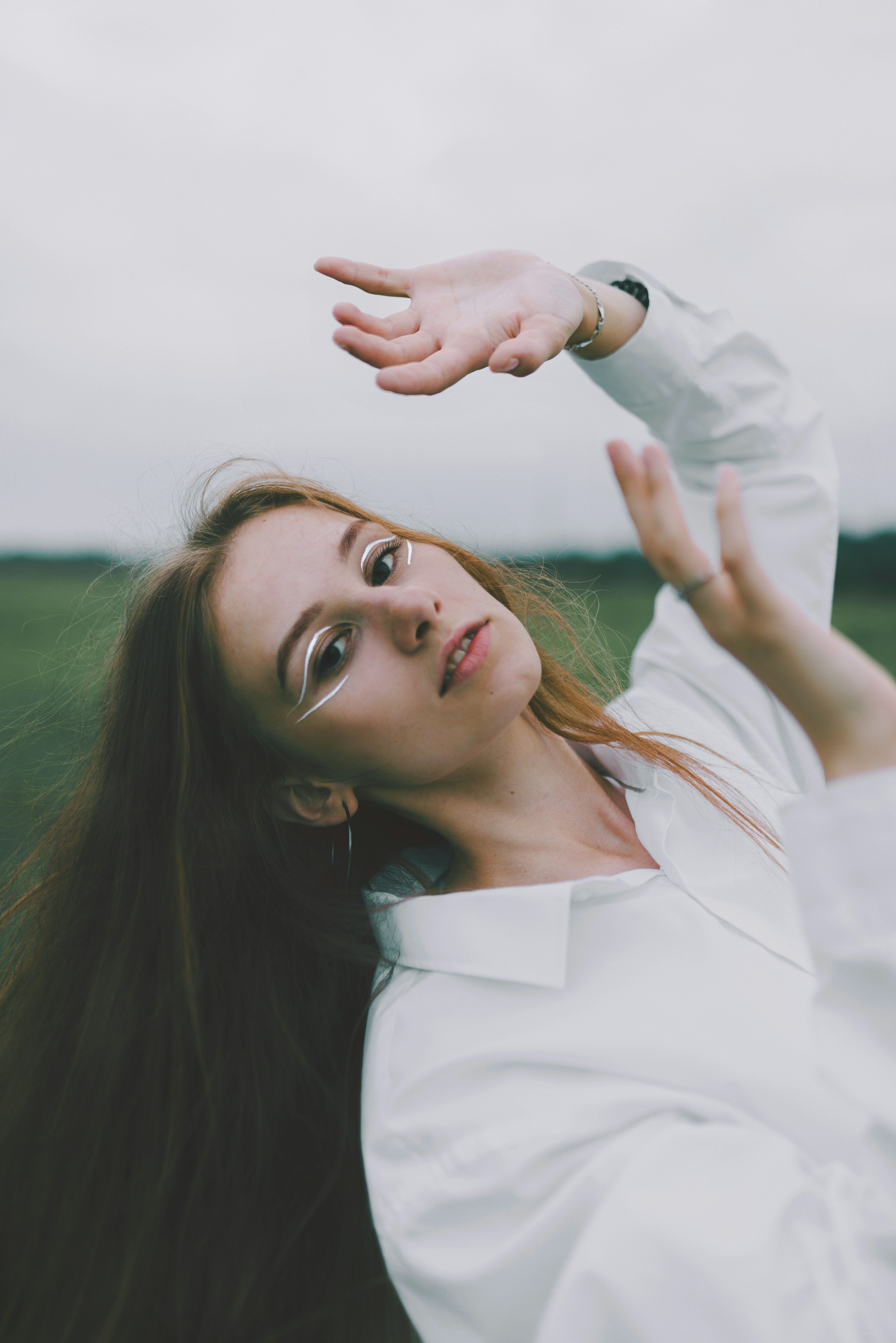 A young woman with flowing hair and striking makeup poses gracefully against a soft, green backdrop.