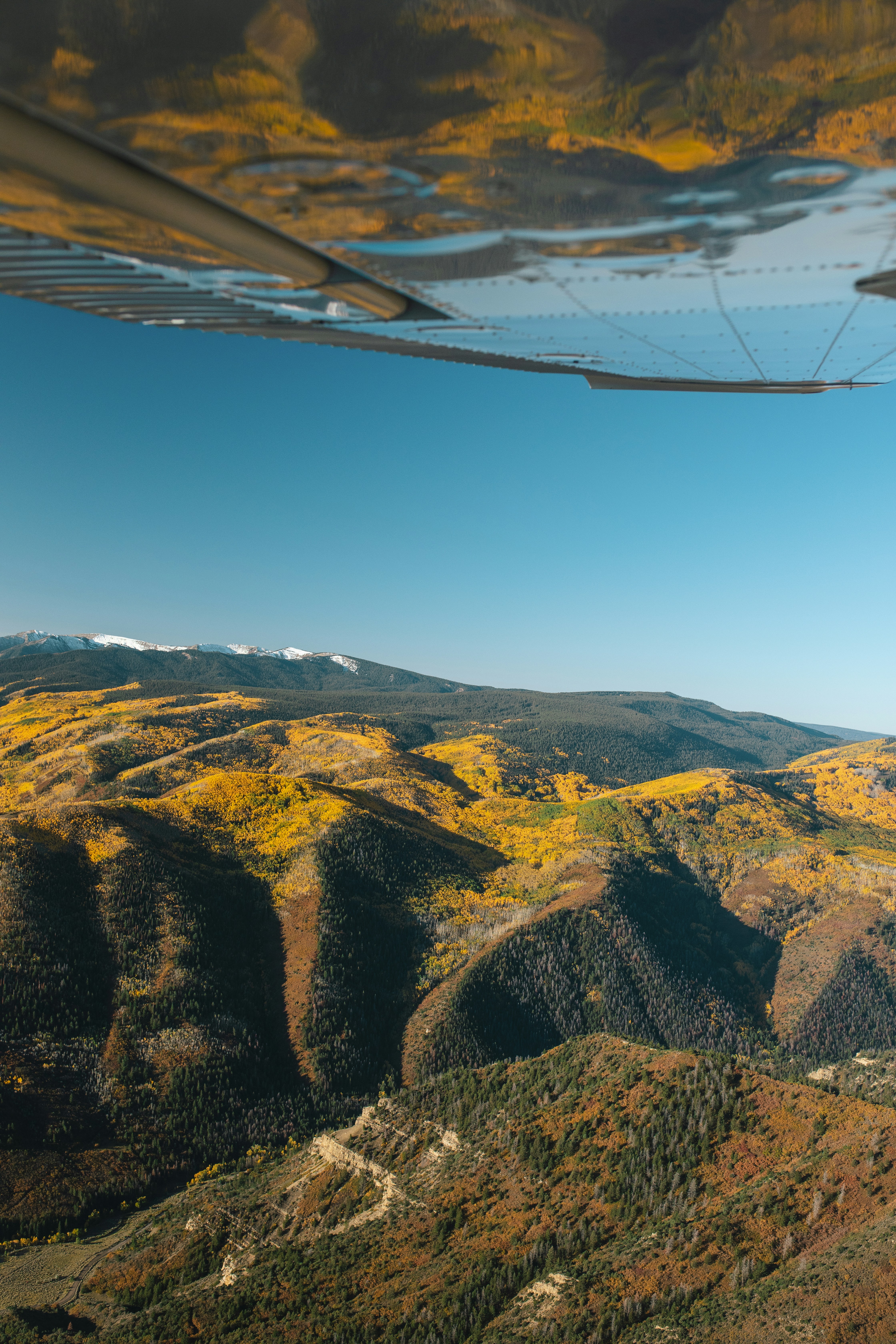 Vibrant autumn landscape viewed from above, showcasing rolling hills adorned with golden and green foliage under a clear blue sky.