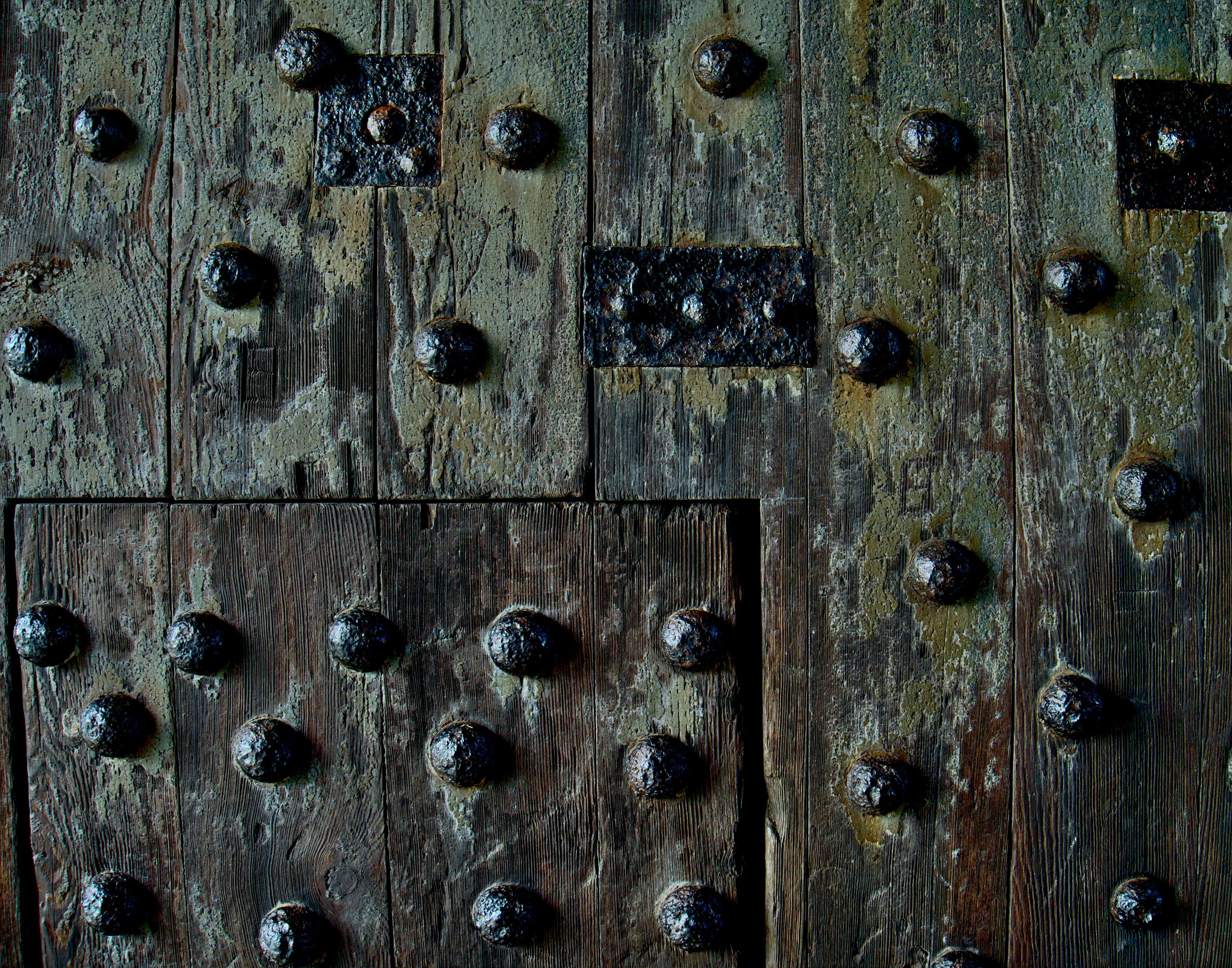 Close-up of an aged wooden gate with prominent metal rivets and weathered textures.