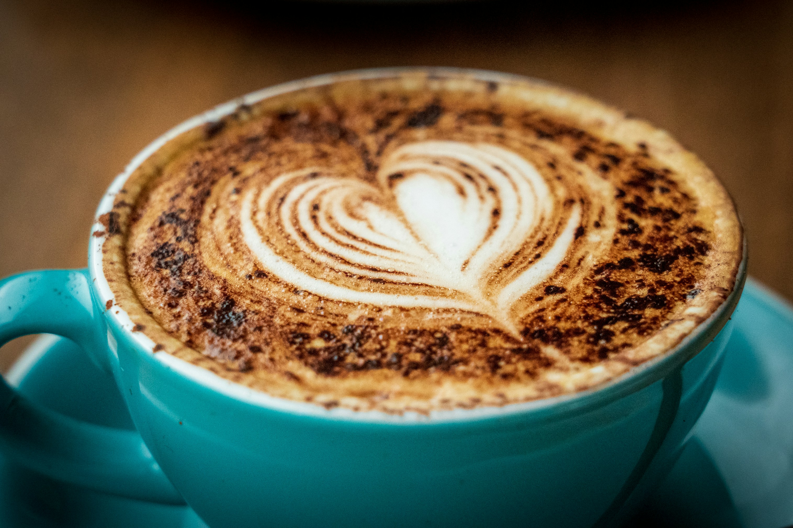 Artfully crafted latte with a heart-shaped foam design in a turquoise cup, resting on a wooden table.