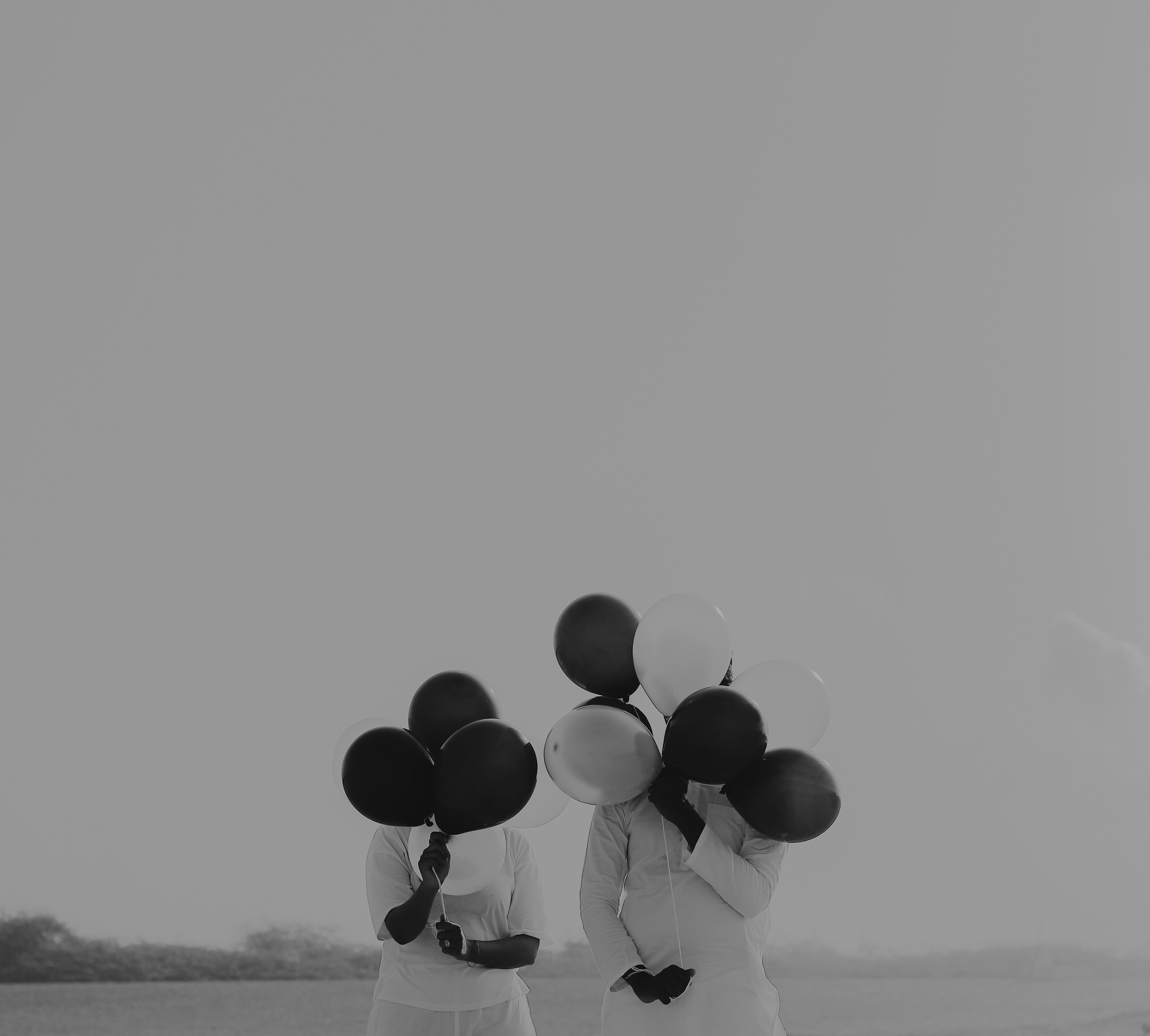 Two individuals in white attire holding black and white balloons against a vast sky backdrop.