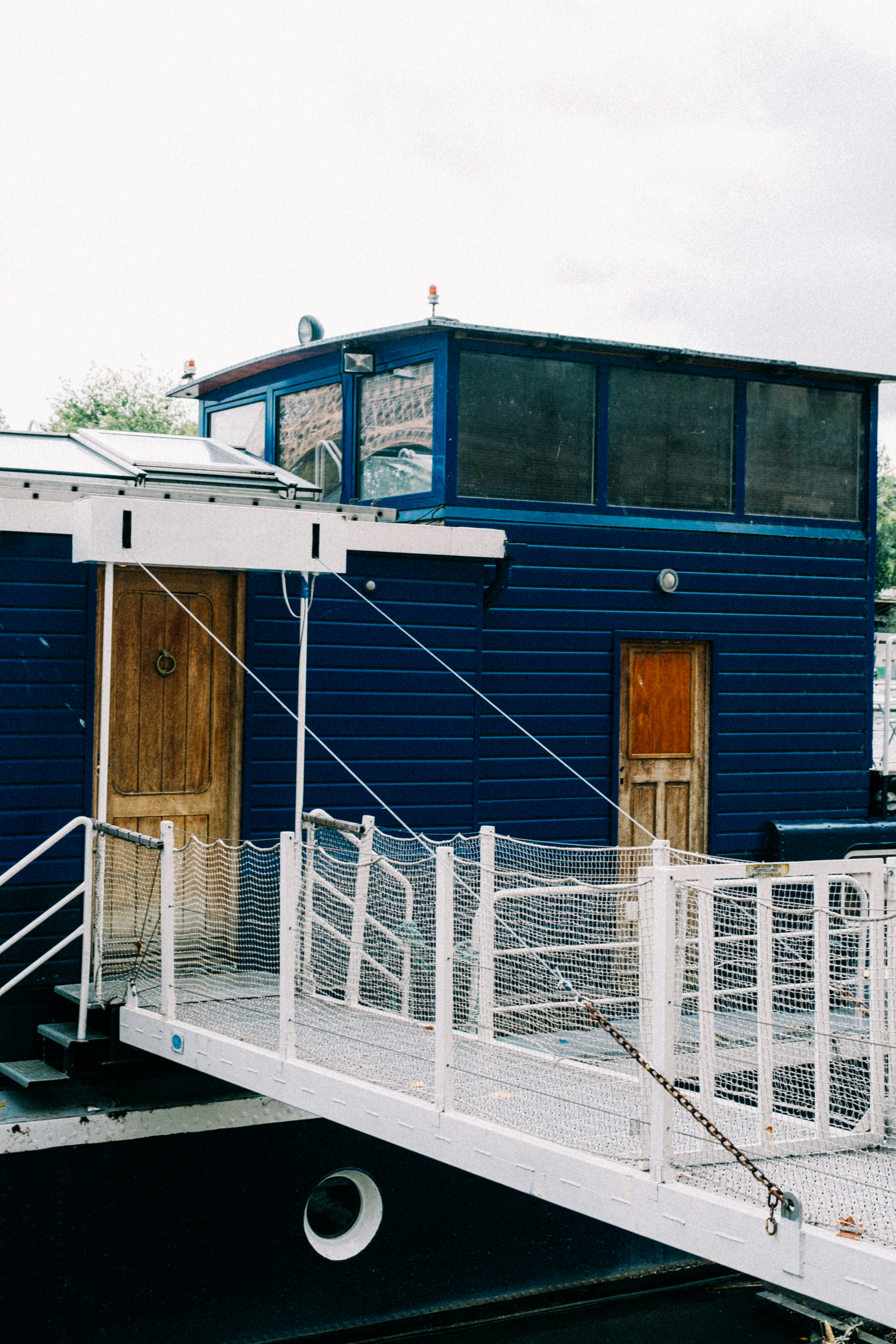 A charming blue houseboat with wooden doors and a mesh walkway leading to it. The scene captures the essence of serene waterfront living.