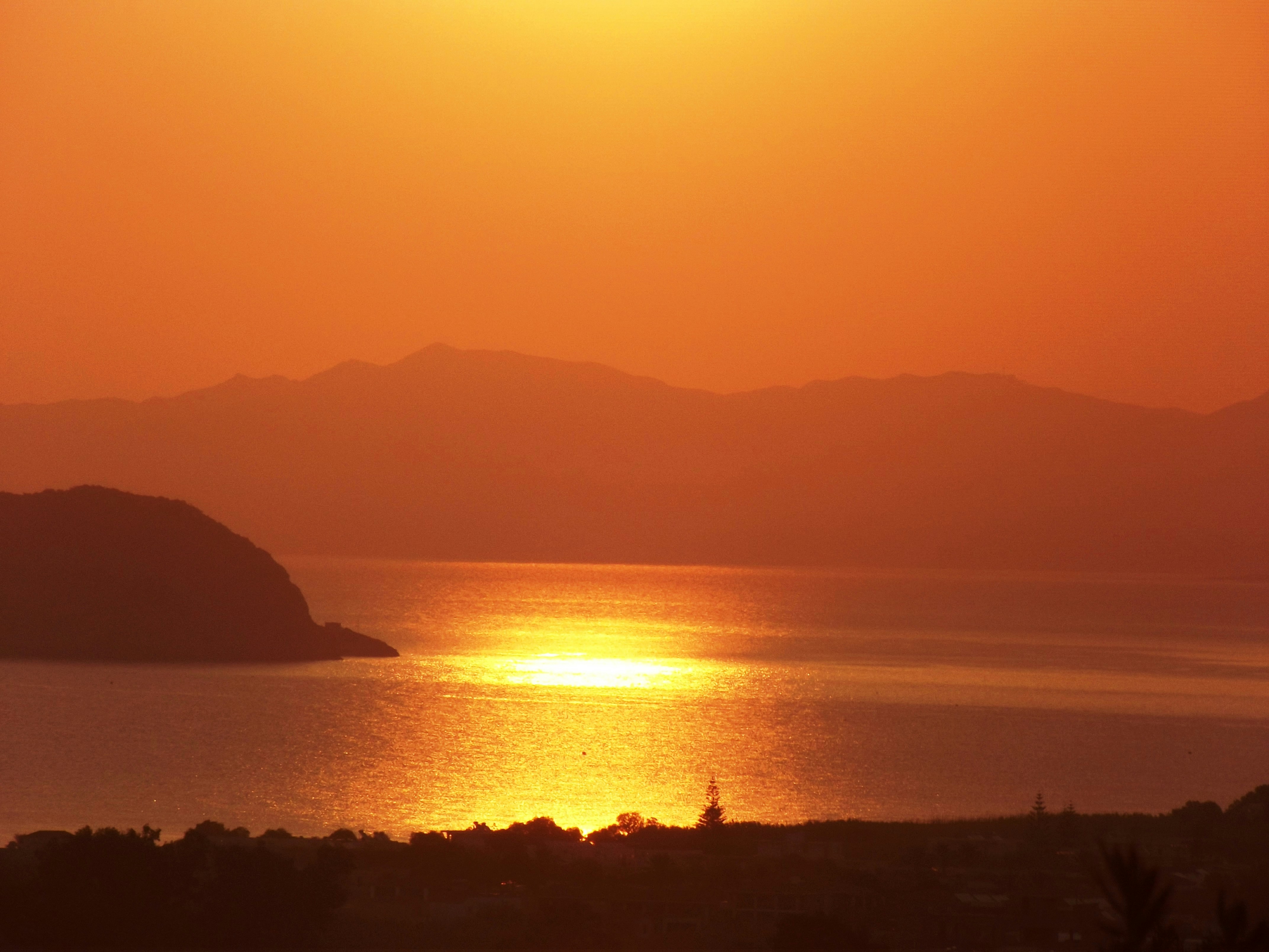 Sunset illuminating a serene body of water, with mountains silhouetted against a vibrant orange sky.